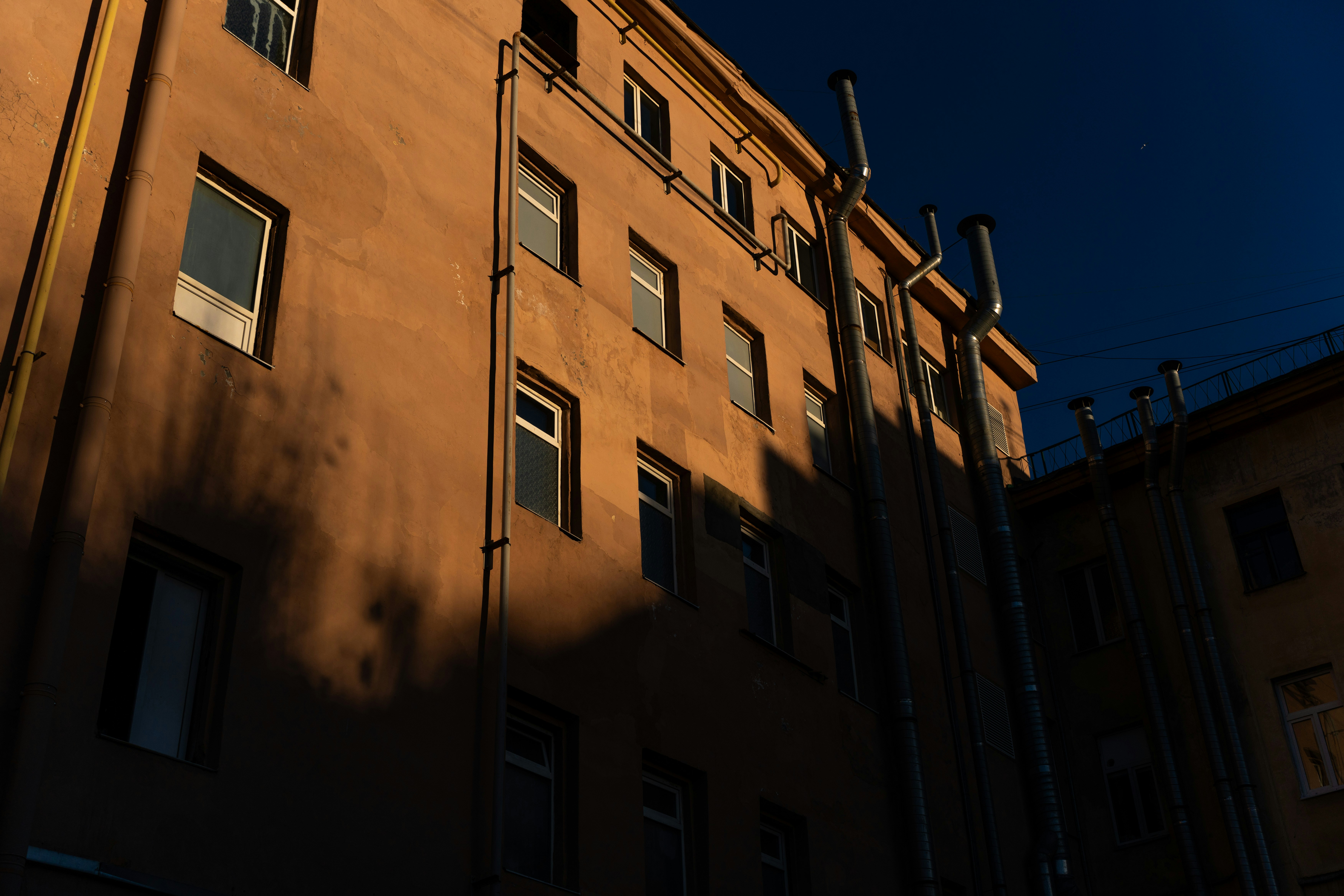 Sunlight casts dramatic shadows on a weathered building, revealing its textured facade and architectural details.