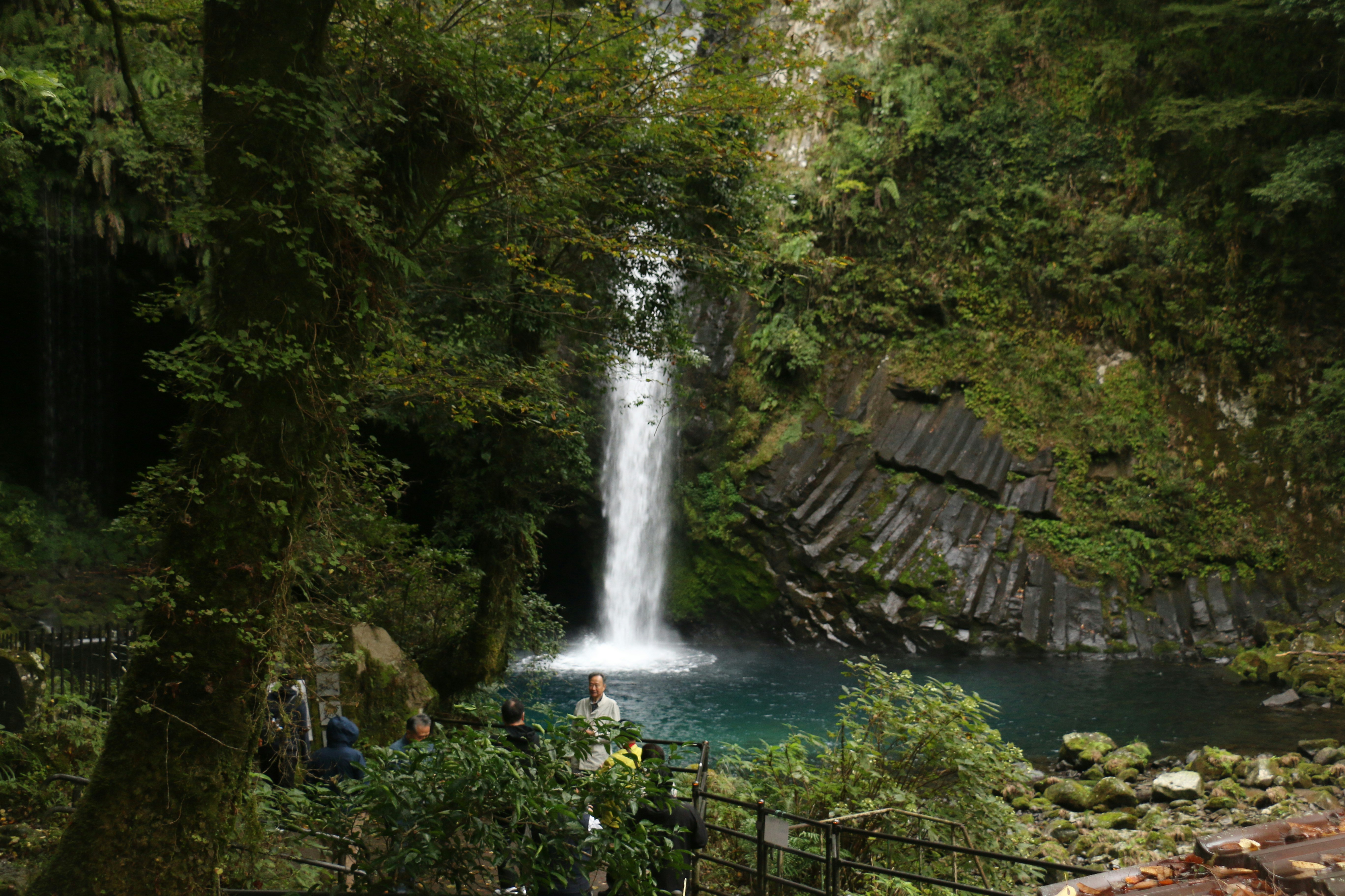 A tall waterfall cascades into a clear blue pool.