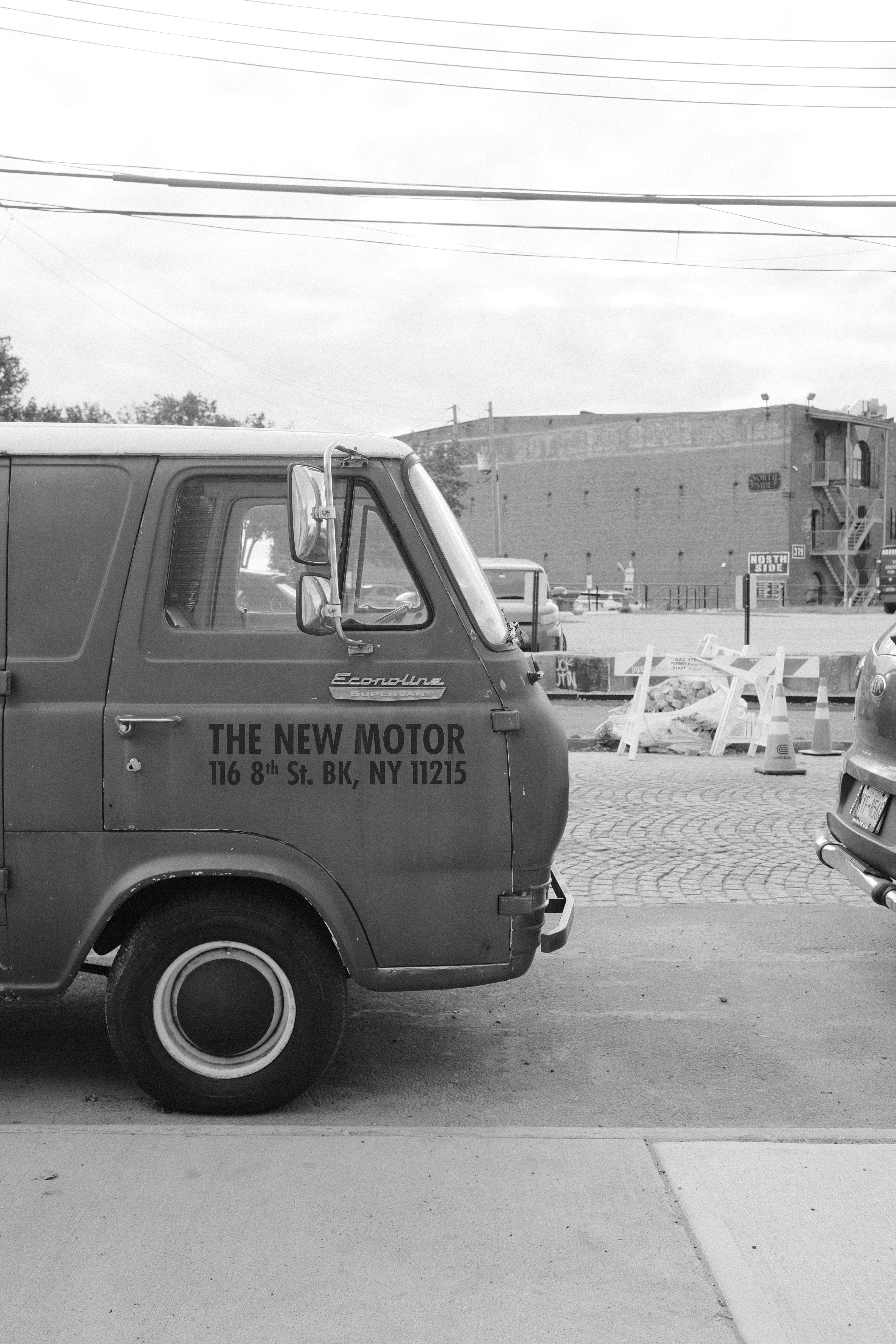 Vintage Econoline van parked on a city street, showcasing its faded signage and classic design. The backdrop features a mix of urban architecture and street elements.