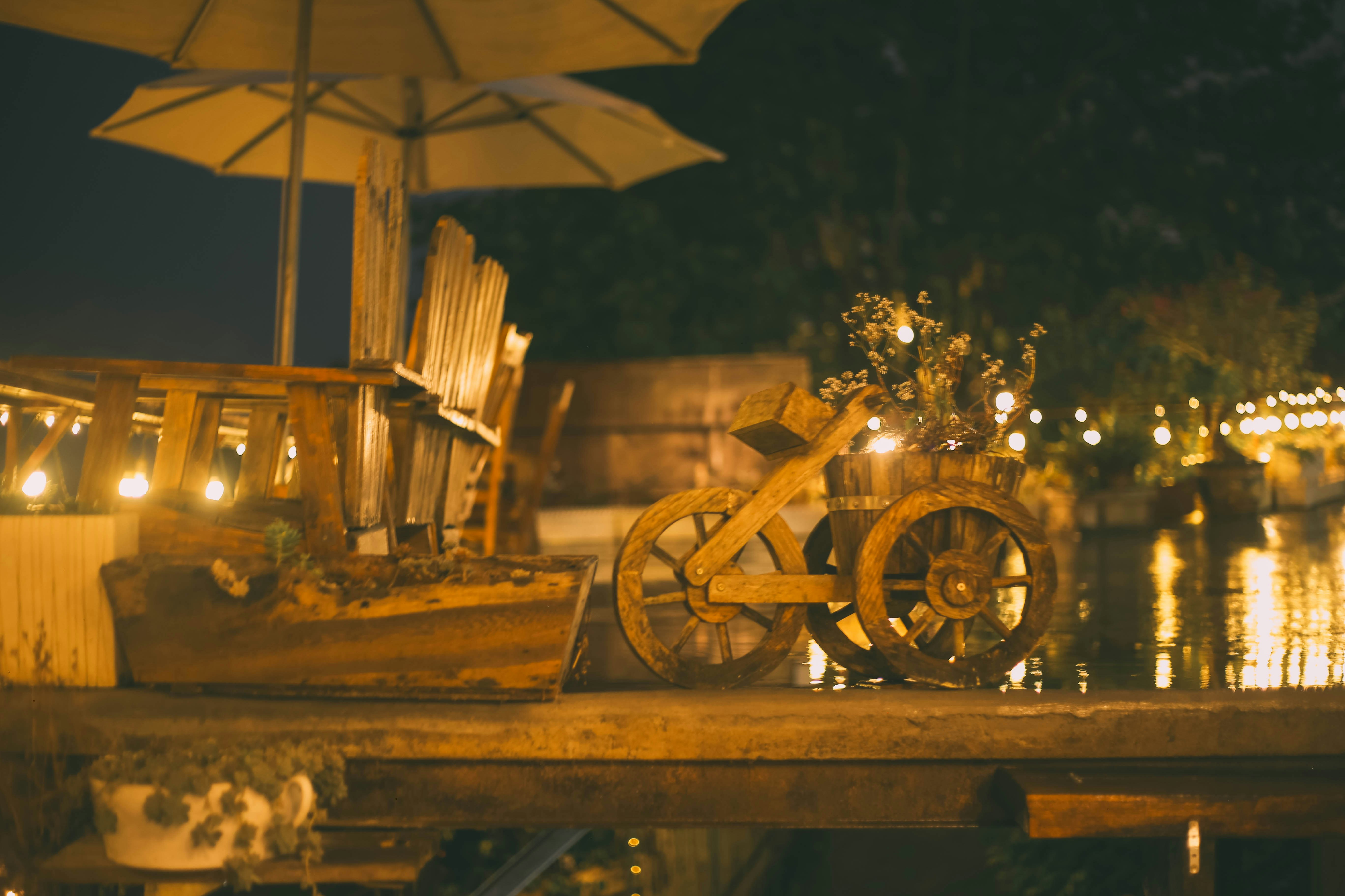 Rustic wooden bicycle planter adorned with flowers, set against a softly lit waterside backdrop at night.