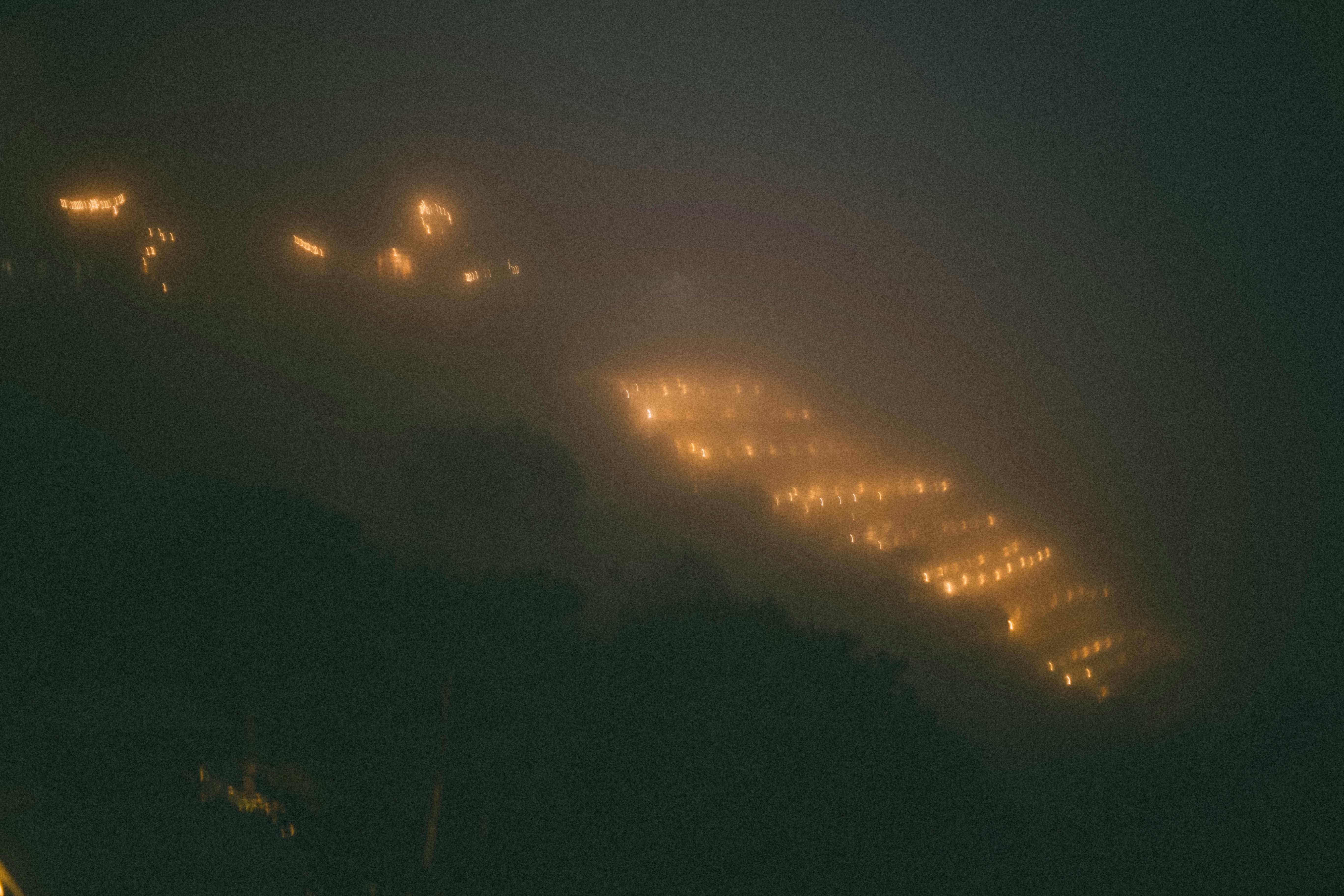 Illuminated terraces emerge from dense fog, creating an ethereal landscape at dusk.