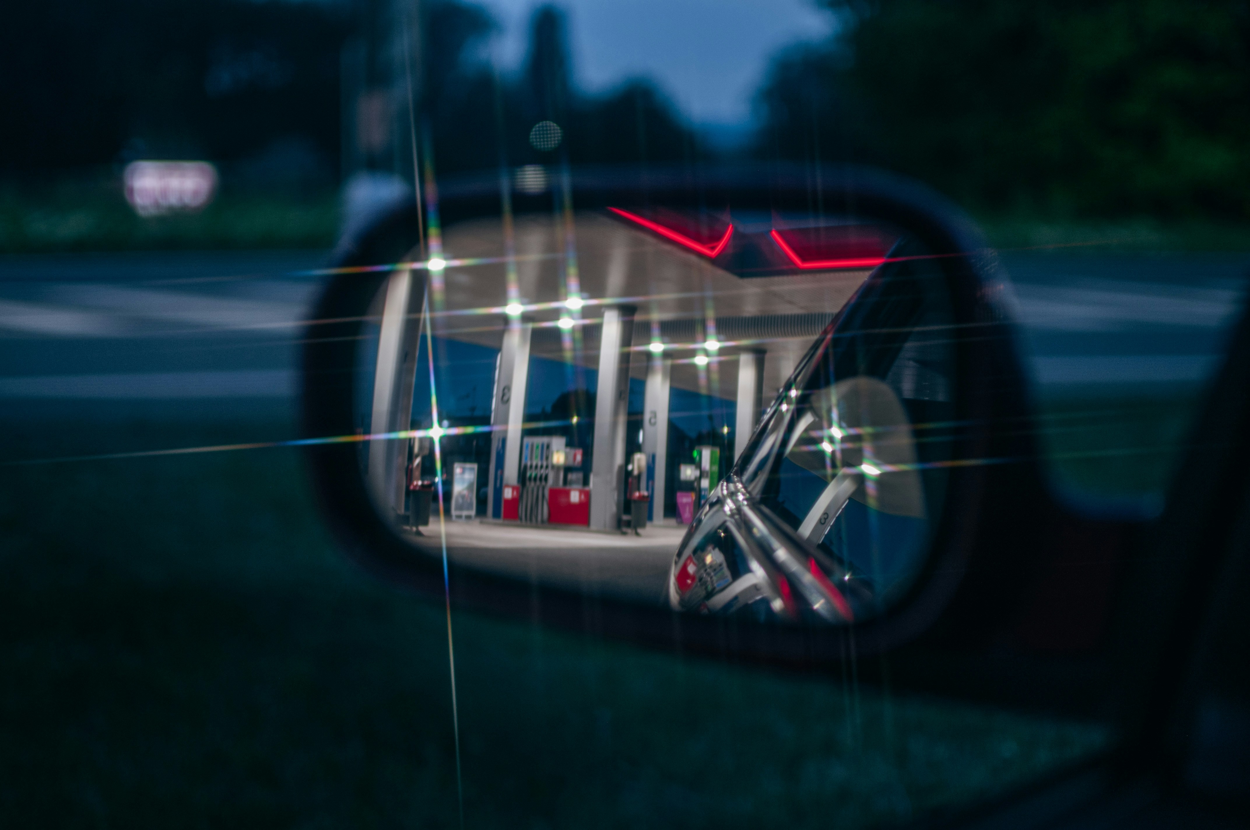 Gas station reflected in a car's side mirror at dusk