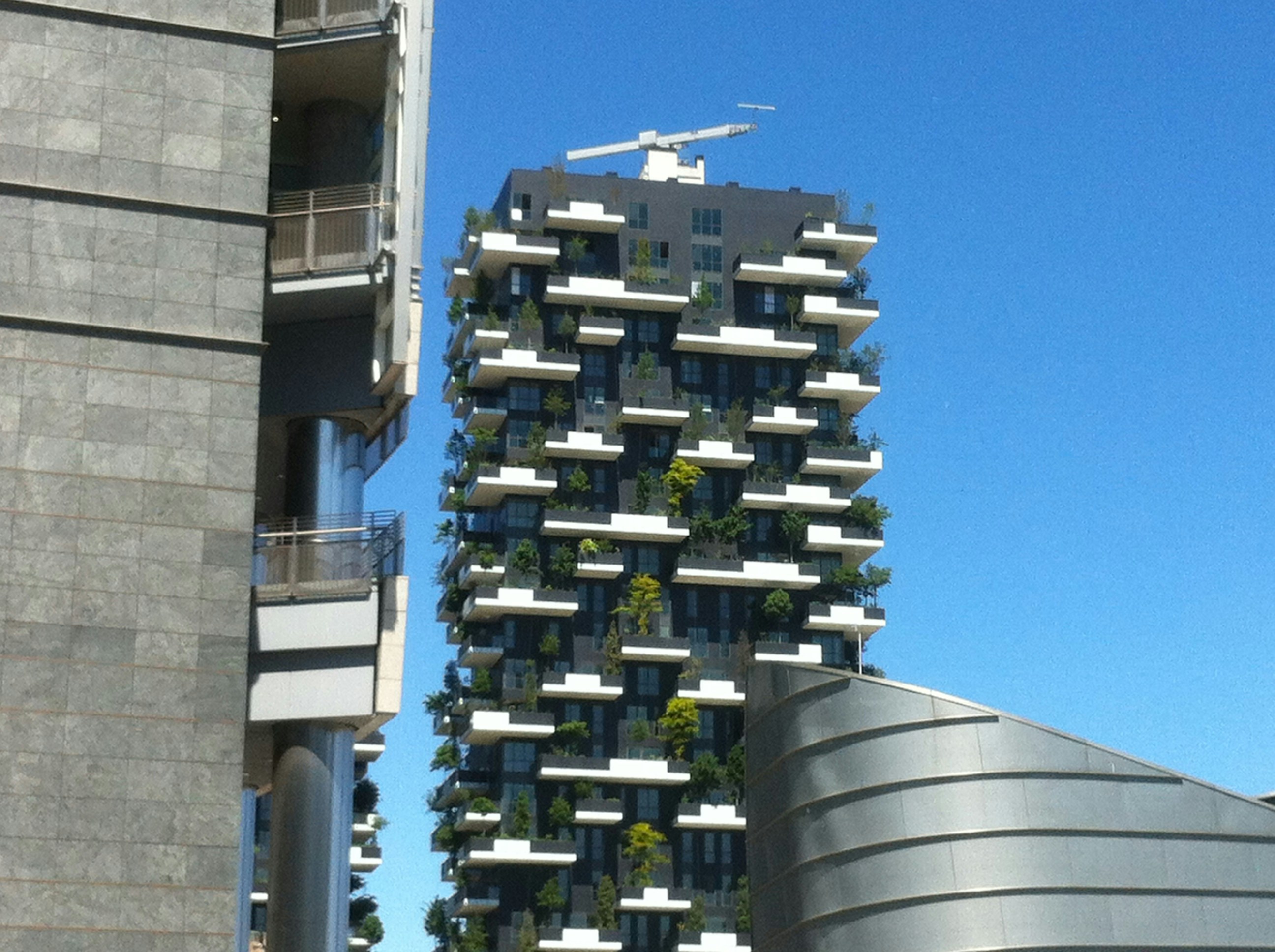 Modern residential building adorned with greenery, showcasing innovative architecture amidst a clear blue sky.