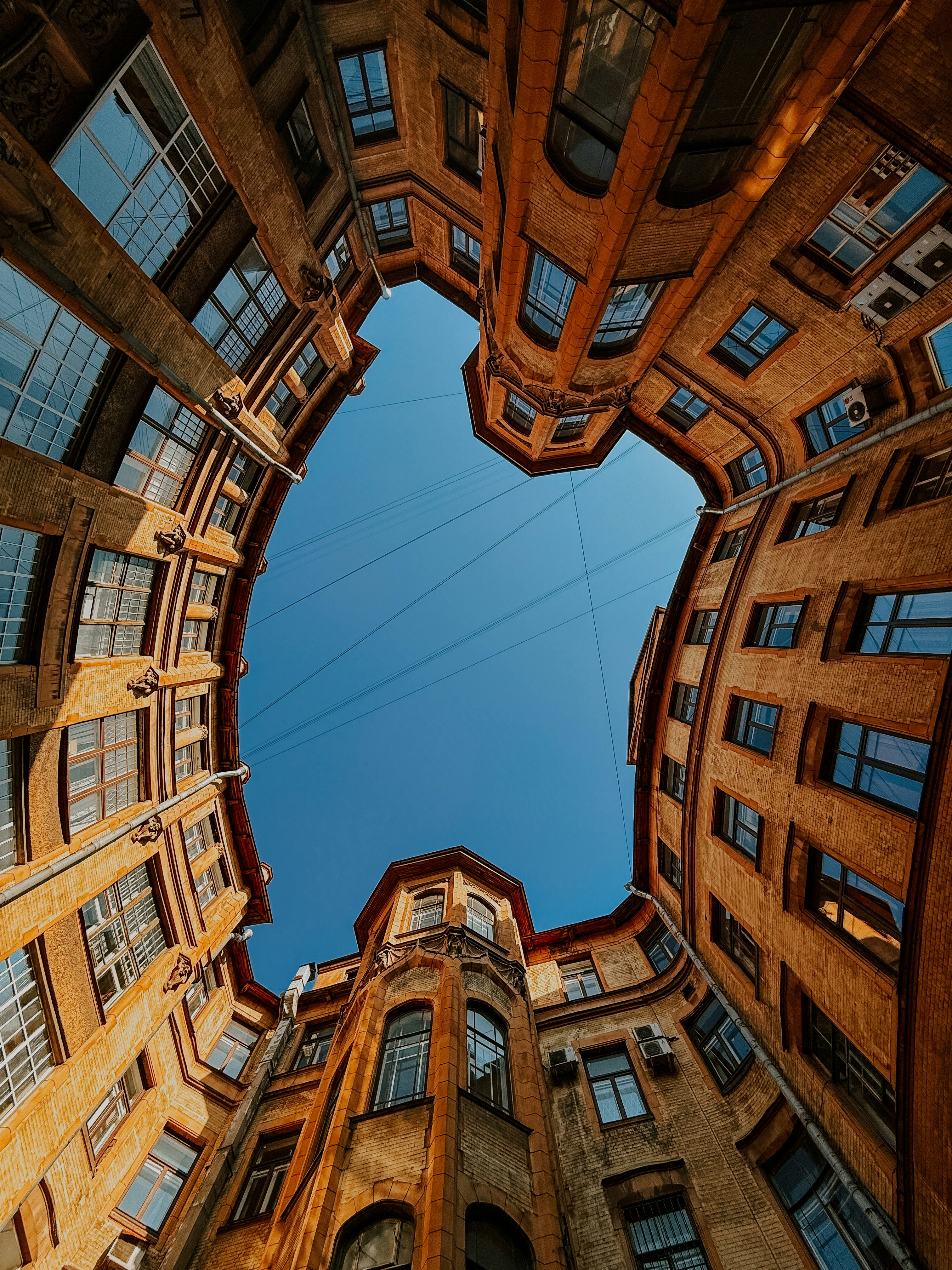 Curved view of a historic courtyard surrounded by ornate brick buildings, leading the eye towards a clear blue sky.