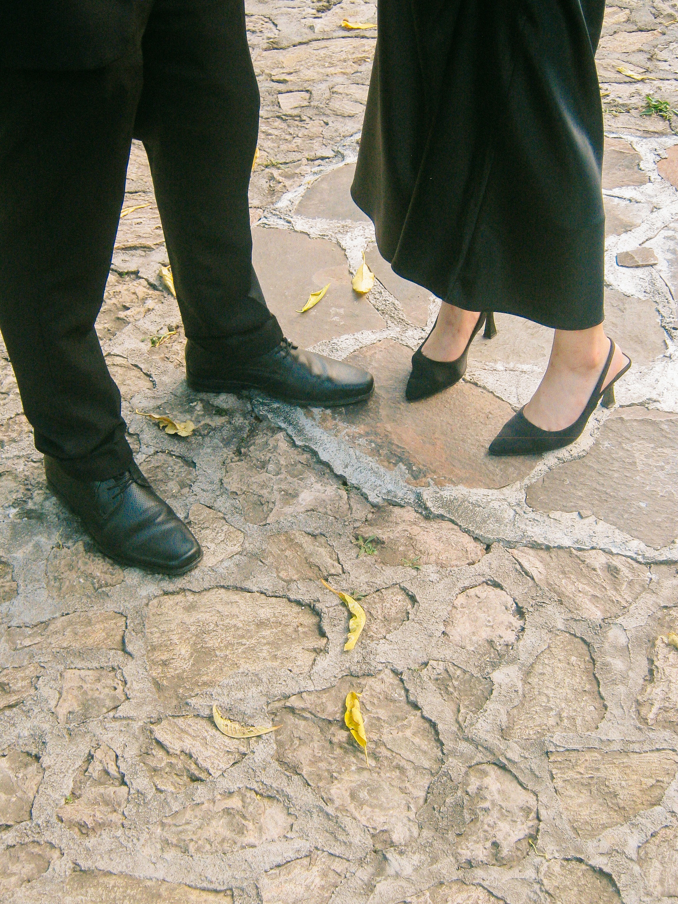 Close-up of elegantly dressed feet on a textured stone surface, highlighting stylish footwear amidst fallen leaves.