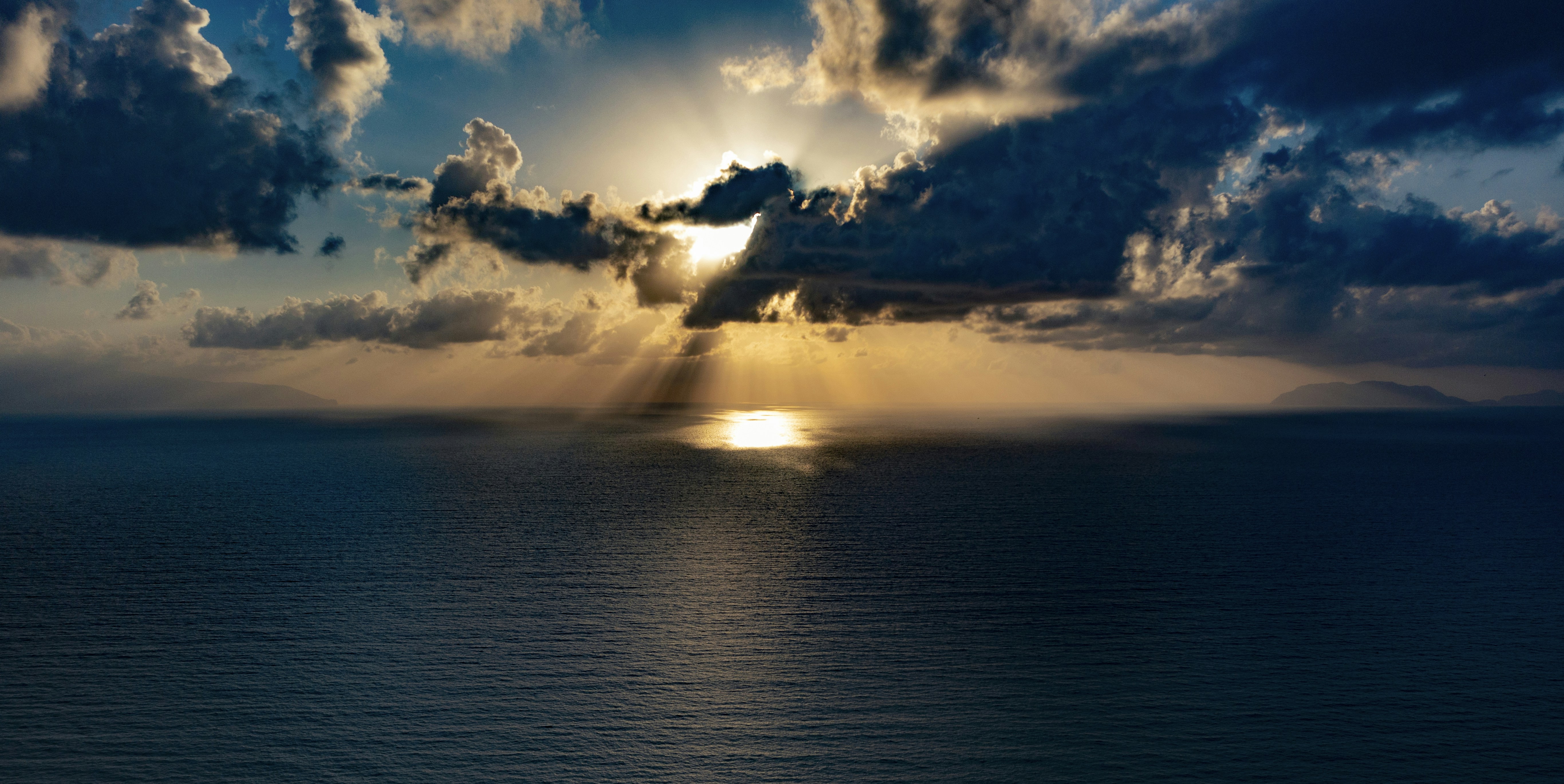 Sunbeams break through clouds over the ocean.