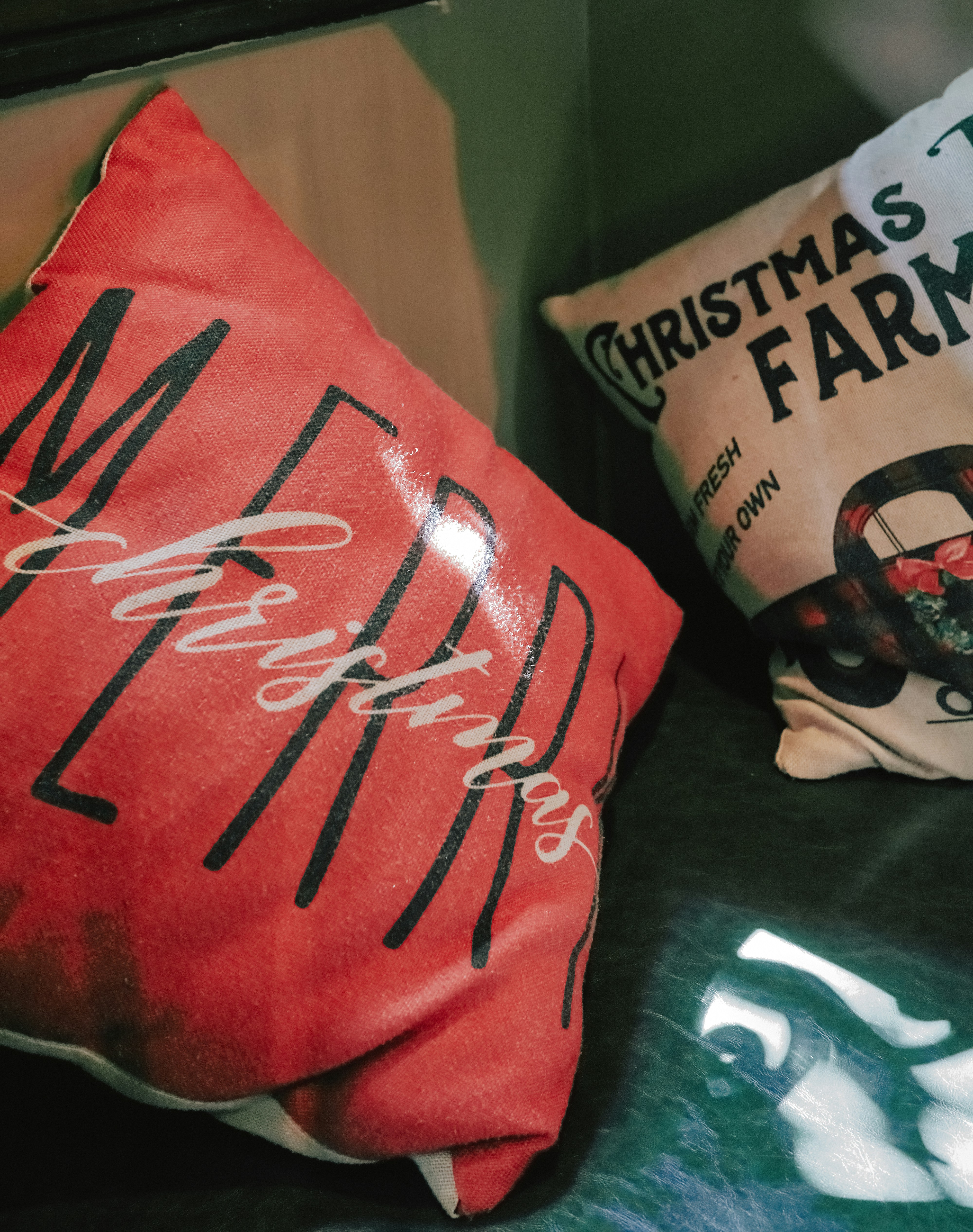 Two decorative pillows on a dark green surface, one with red fabric and the words “Merry Christmas,” and another with a “Christmas Farm” print, both featuring holiday-themed designs. | Two christmas themed pillows on a dark surface