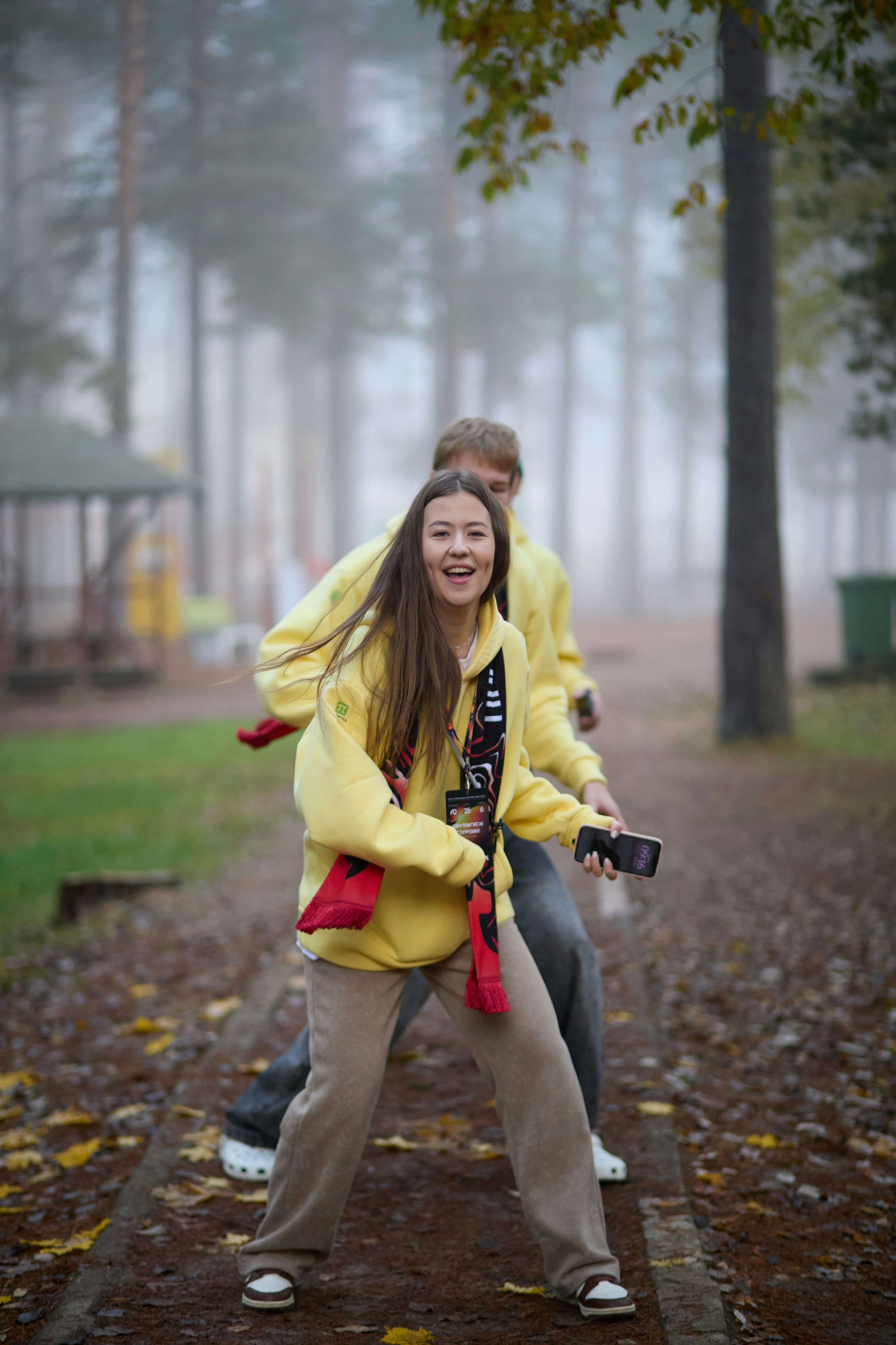 Two young people in yellow hoodies in a foggy forest.