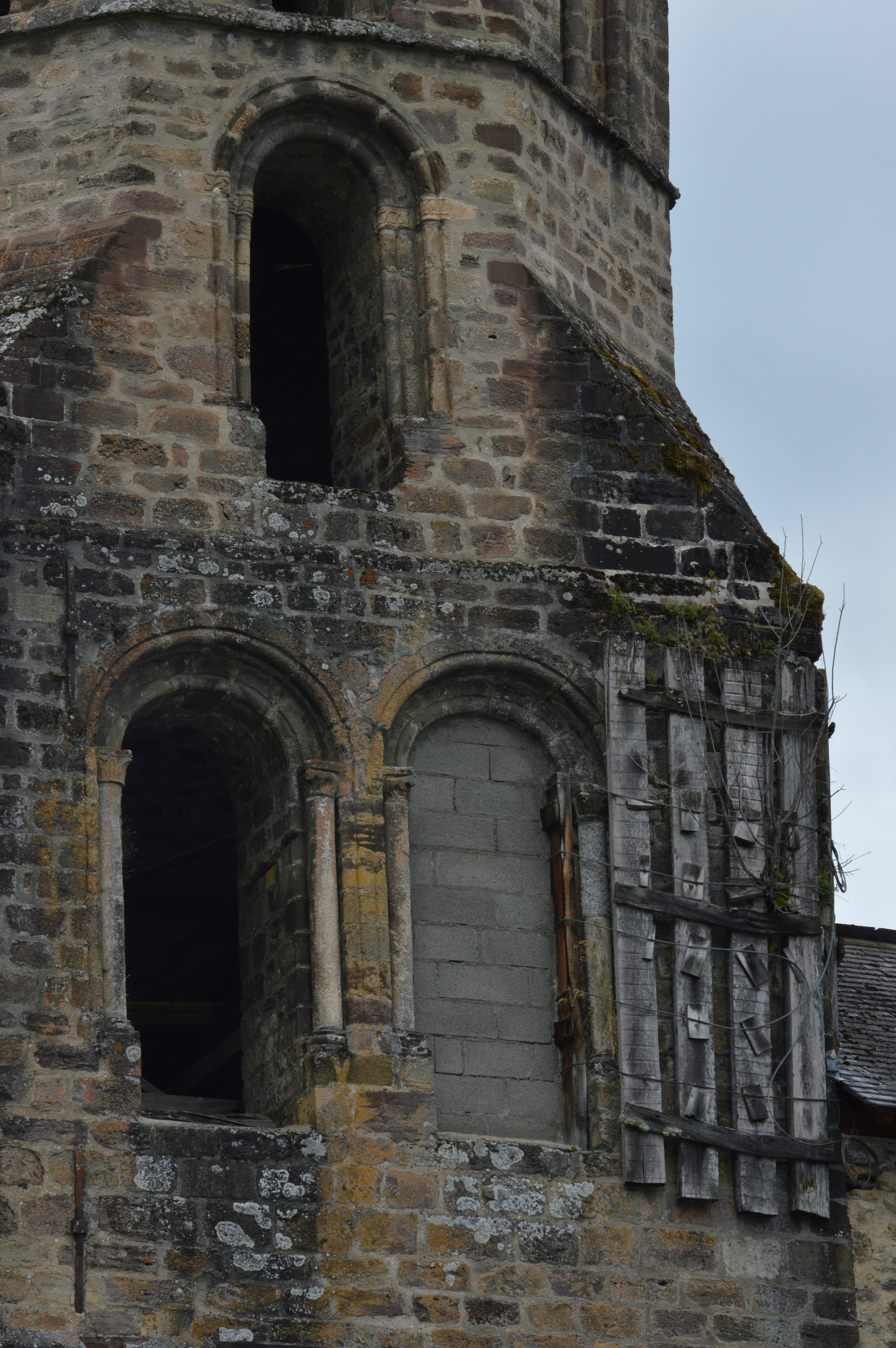 Ancient stone tower with arched windows and weathered wooden shutters, showcasing the passage of time and nature's reclaiming touch.