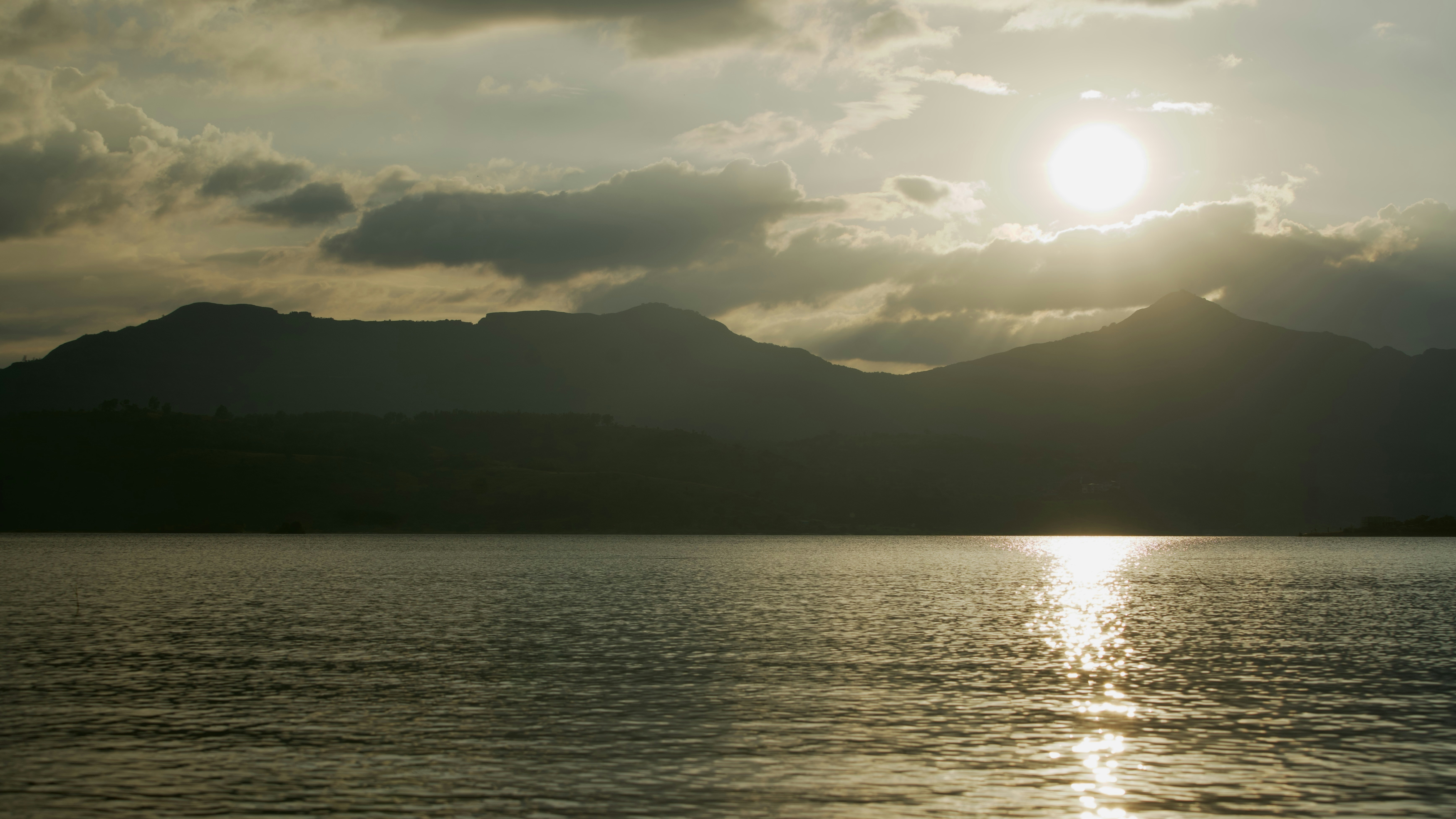 Golden sun setting behind mountains, casting reflections on a calm lake surface. A serene landscape invites contemplation.