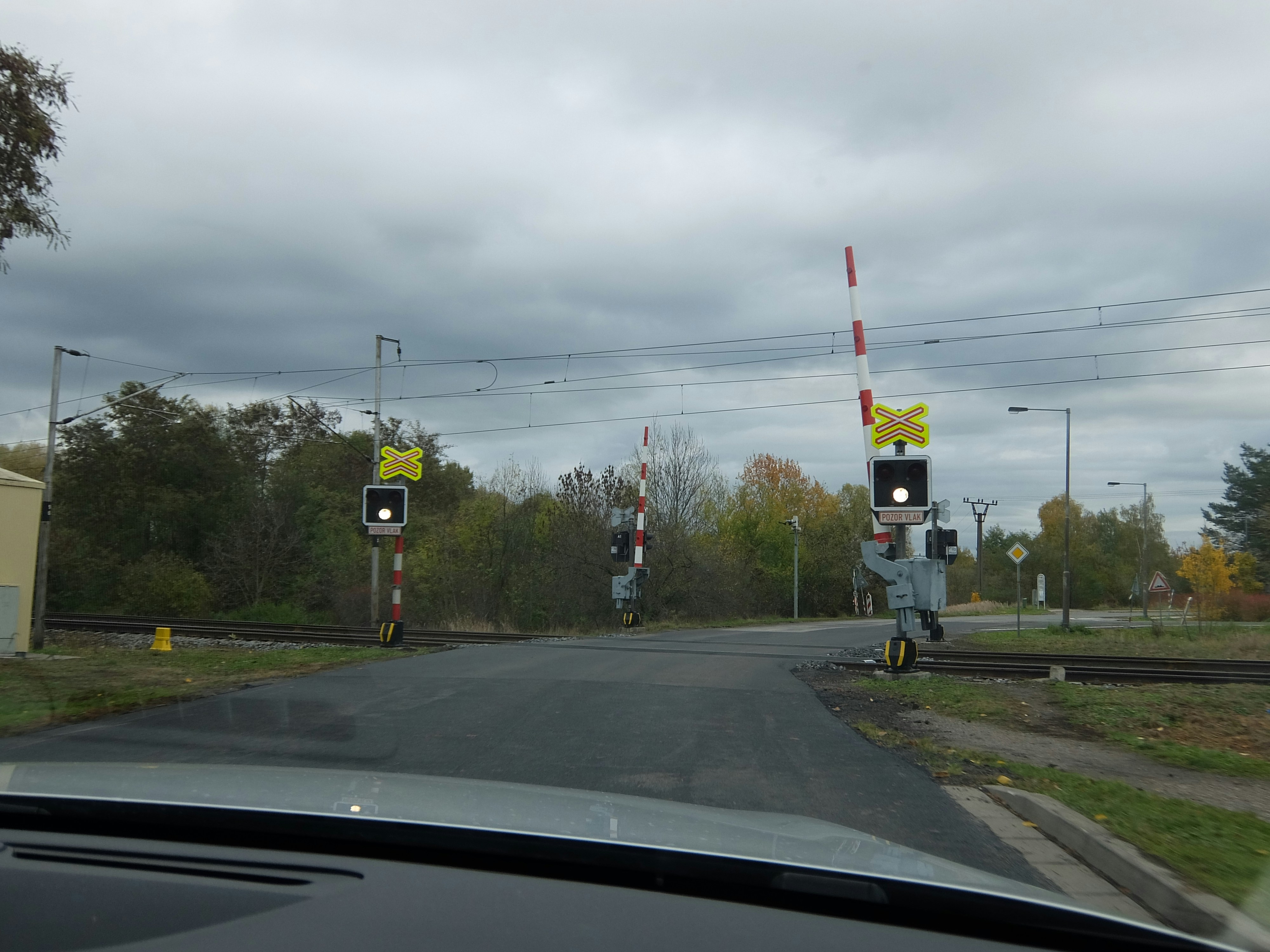 Railroad crossing signals positioned at a junction, alerting drivers to the approaching train. The surrounding landscape features autumn foliage.