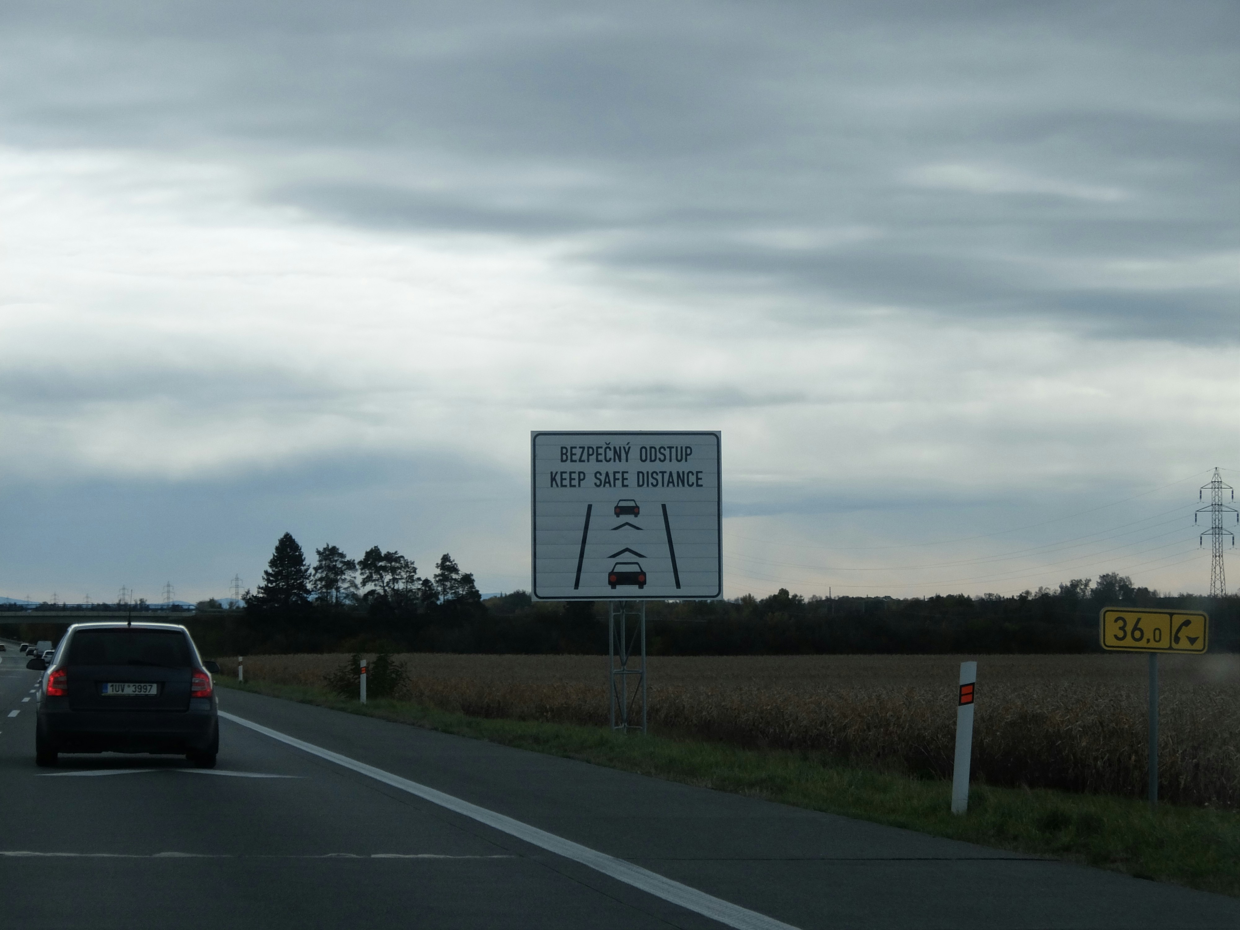Road sign reminding drivers to maintain a safe distance, with a vehicle in the foreground and a cloudy sky overhead.