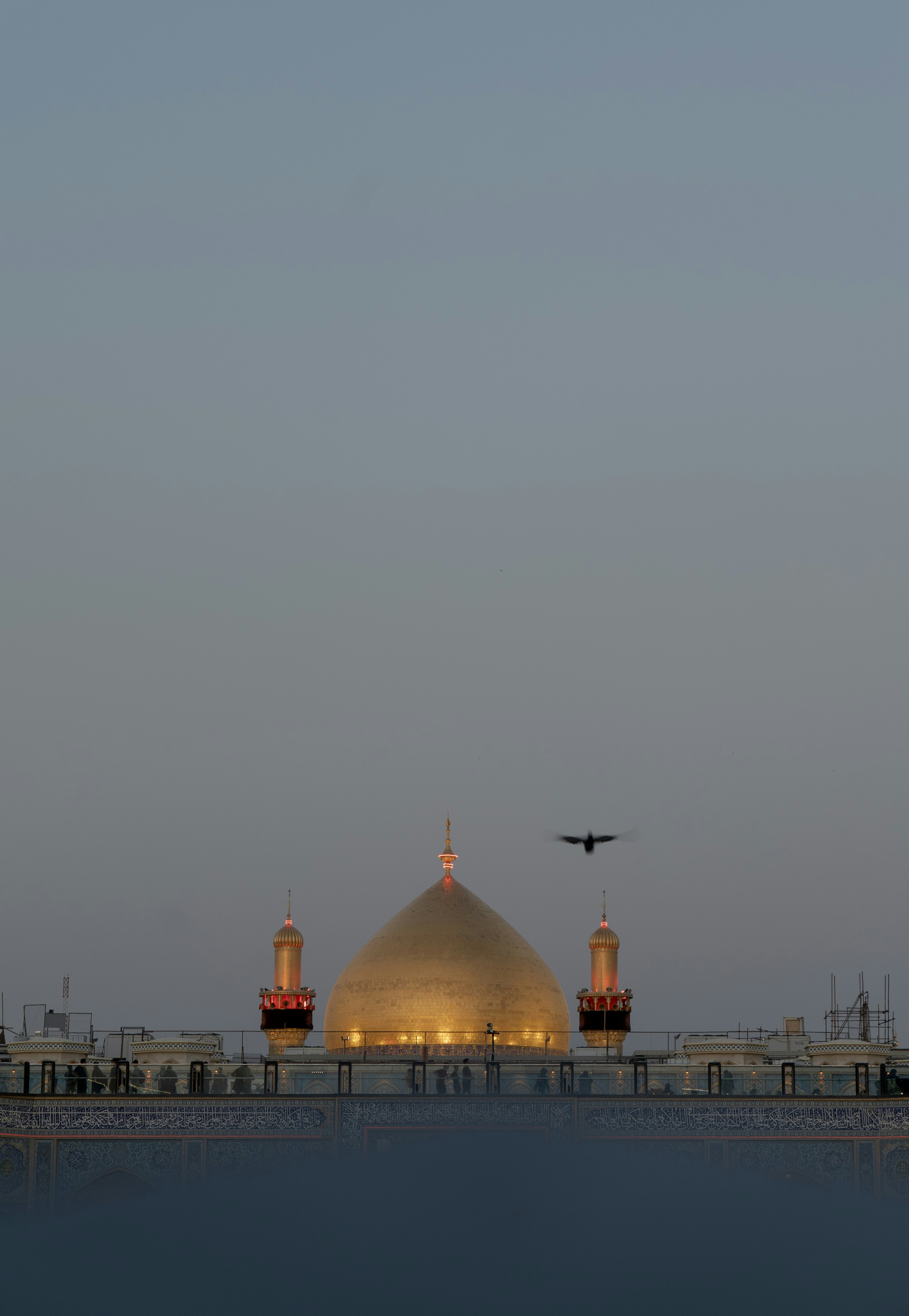 Illuminated dome of a historical structure at dusk, surrounded by a serene atmosphere. A bird flies gracefully in the foreground.