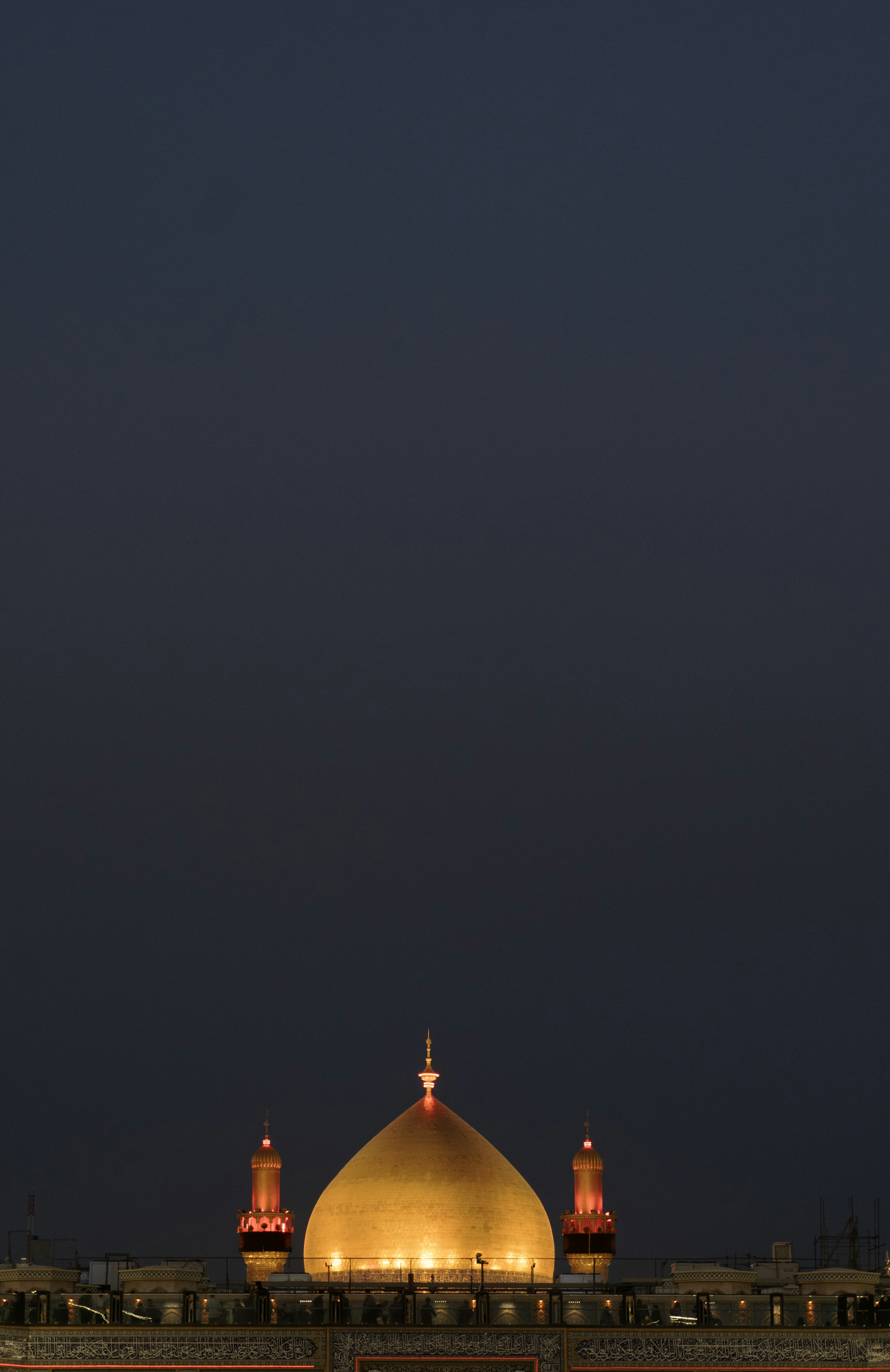 Holy shrine of Imam Ali pbuh, Najaf arbaeen | Golden dome and minarets illuminated against dark sky.