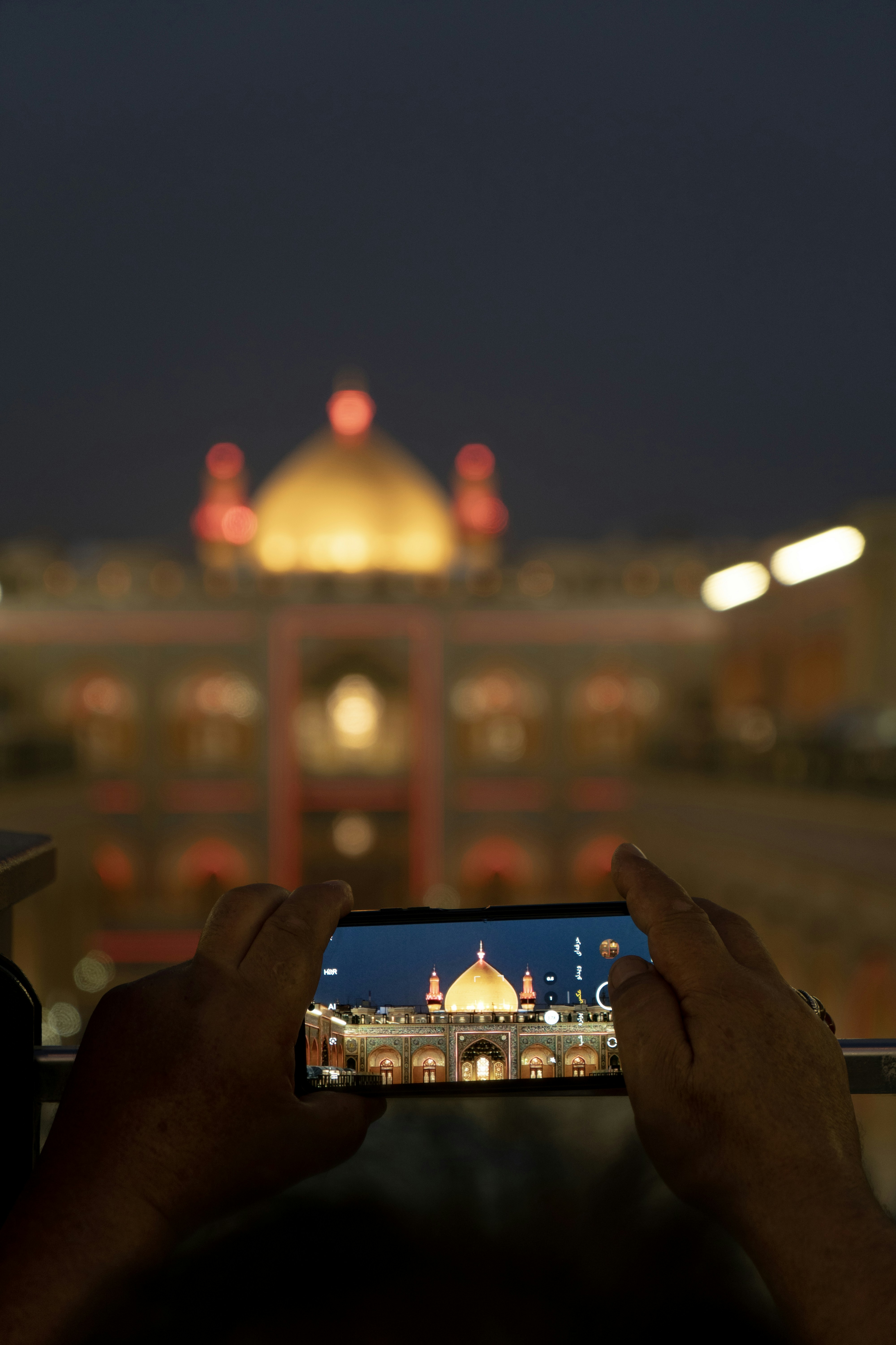 Holy shrine of Imam Ali pbuh, Najaf arbaeen | Hands holding phone capturing illuminated building at night