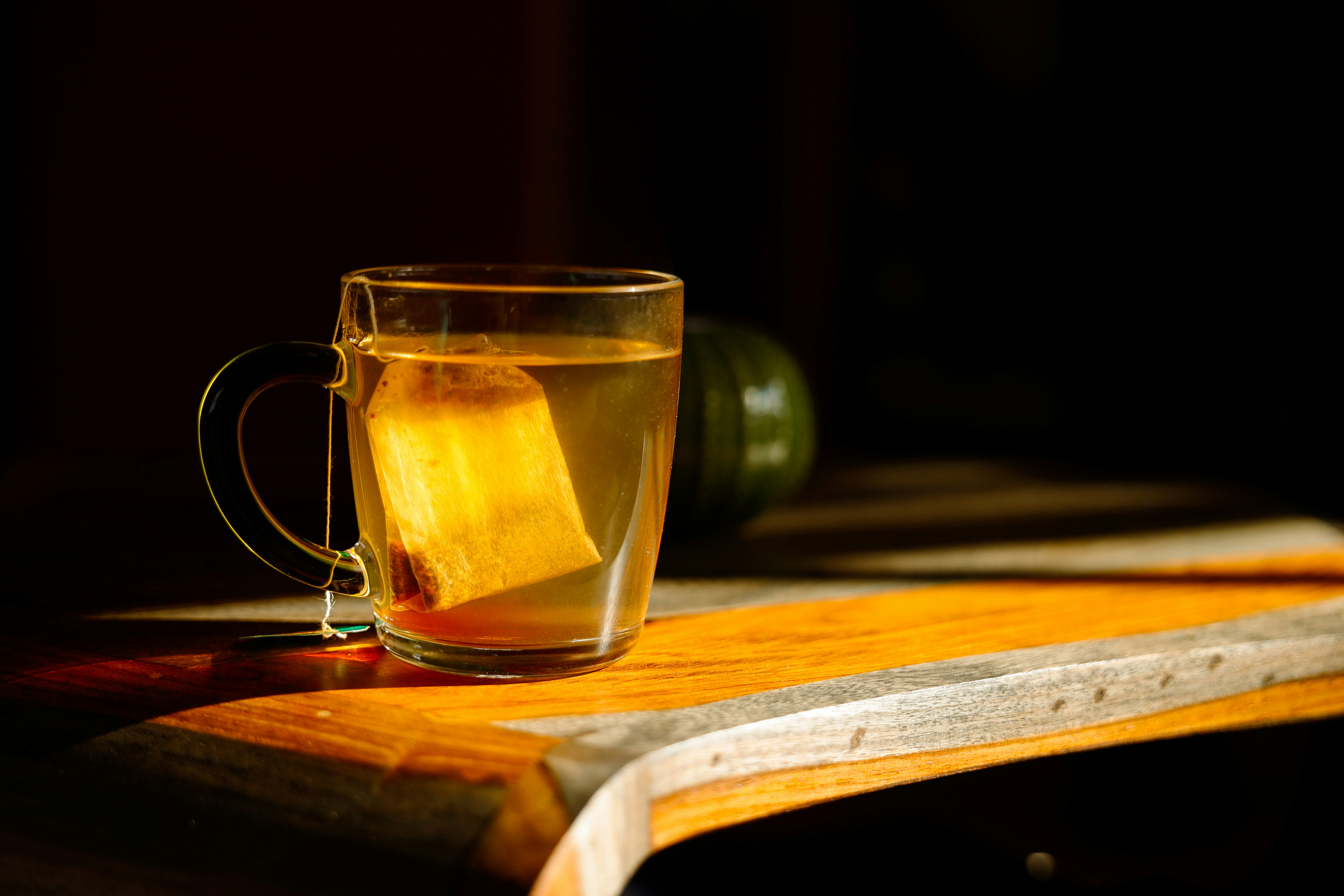 Clear glass mug filled with herbal tea, featuring a tea bag steeping in warm water. The scene is illuminated by soft natural light.