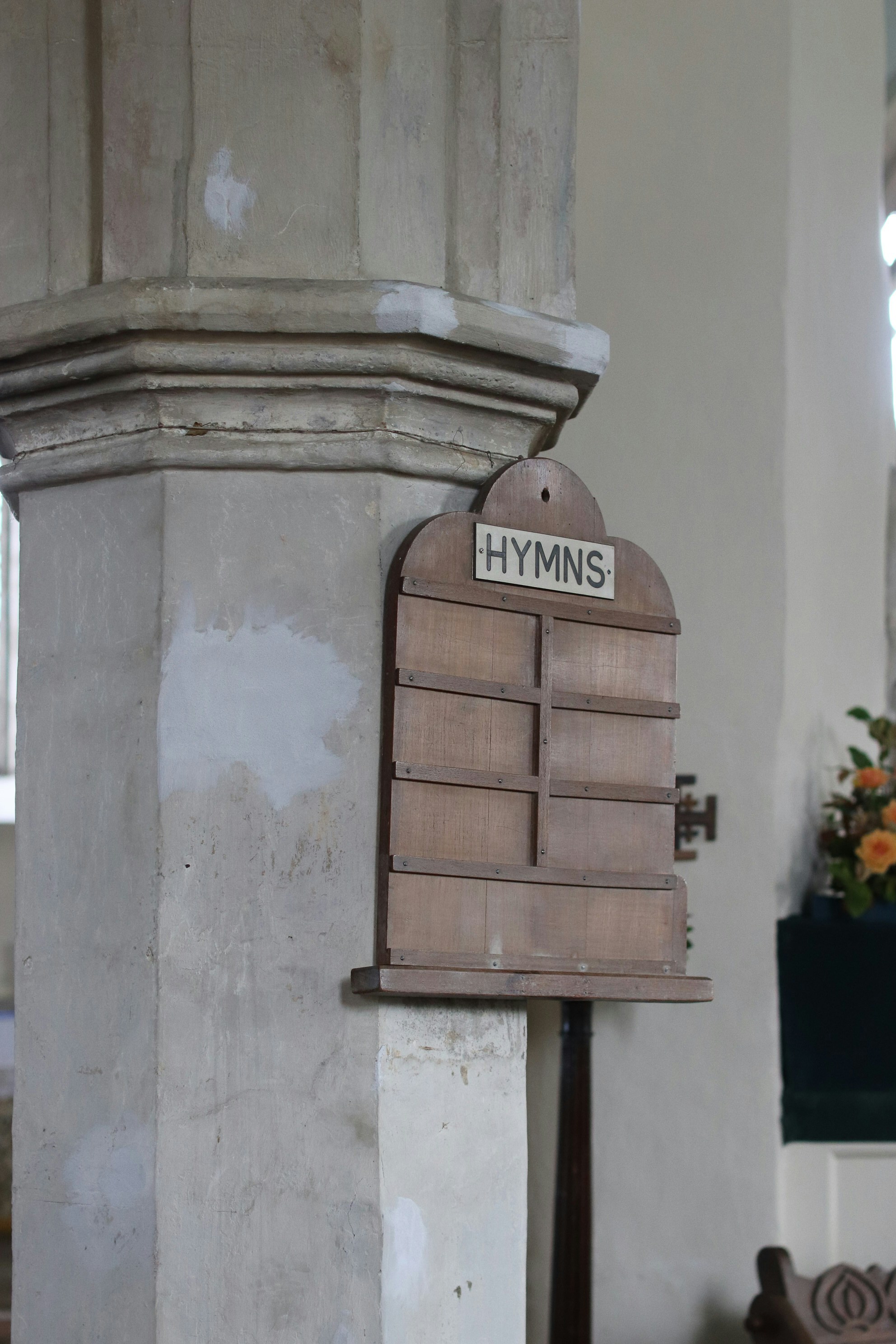 Wooden hymn board mounted on a church pillar, featuring blank slots for hymn titles. The setting reflects a serene and historical ambiance.