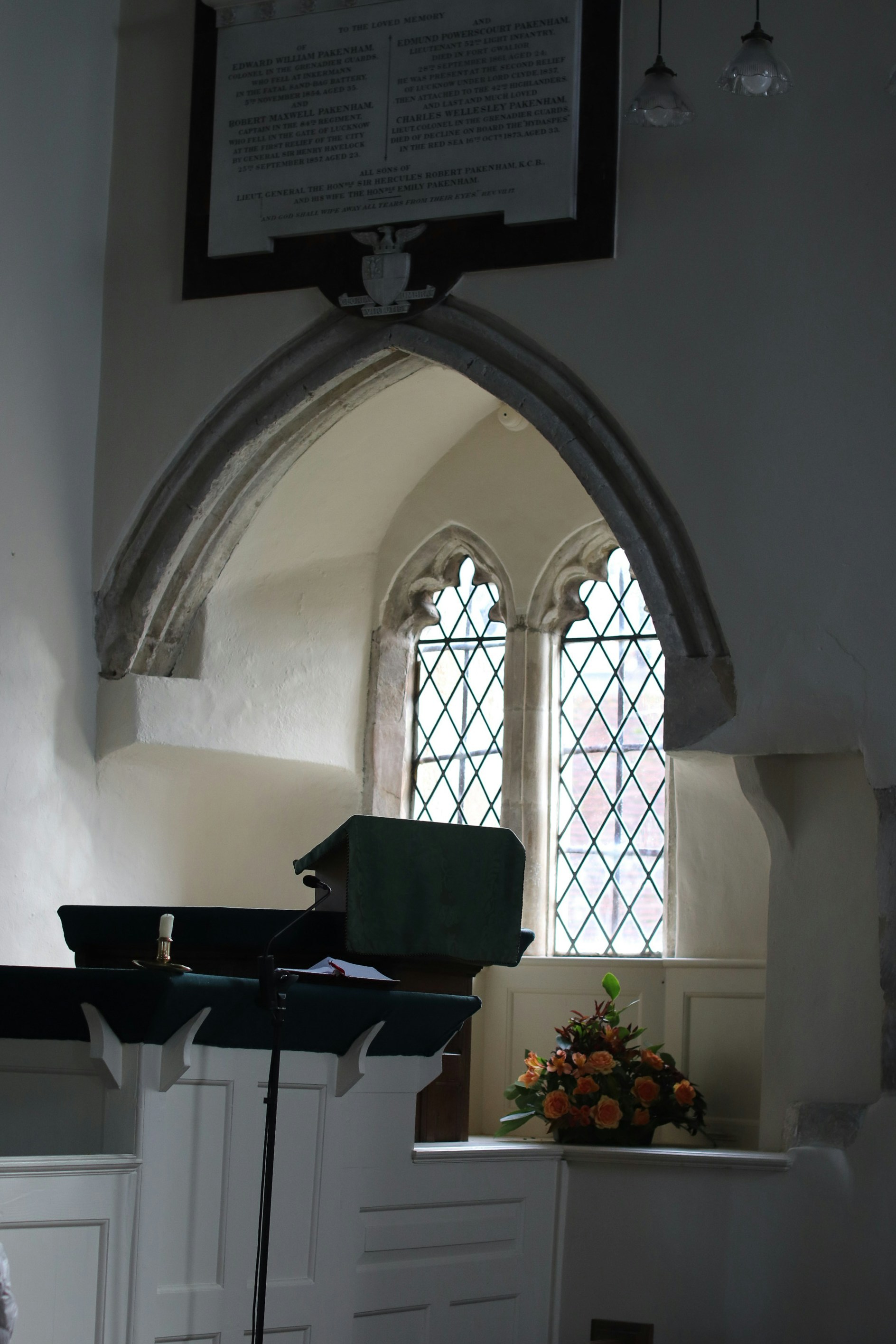 Gothic archway leading to a stained glass window, framed by soft light and floral arrangements. A pulpit stands ready for reflection.