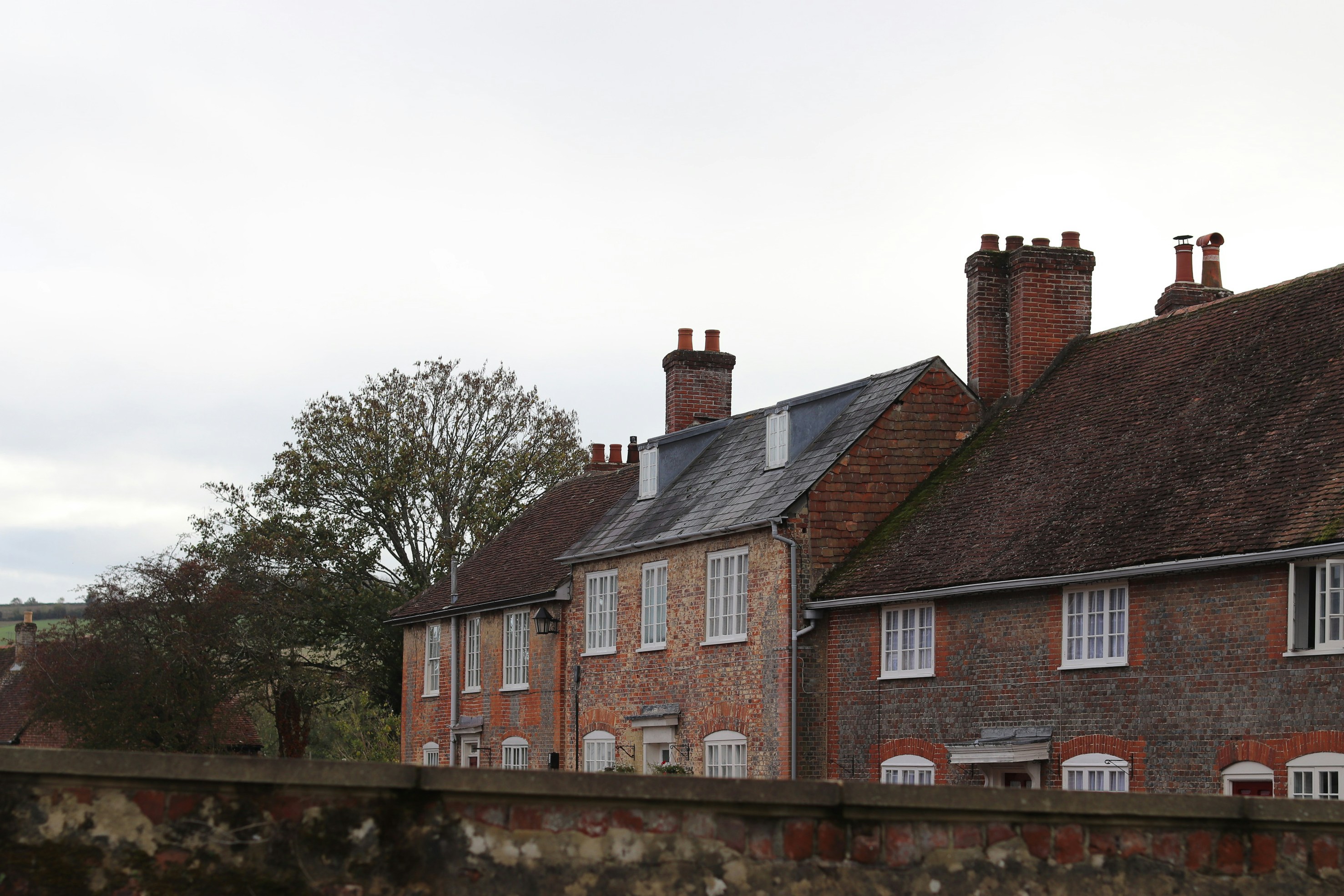 Charming brick houses with distinctive chimneys nestled against a cloudy sky, showcasing a blend of architectural styles and natural surroundings.