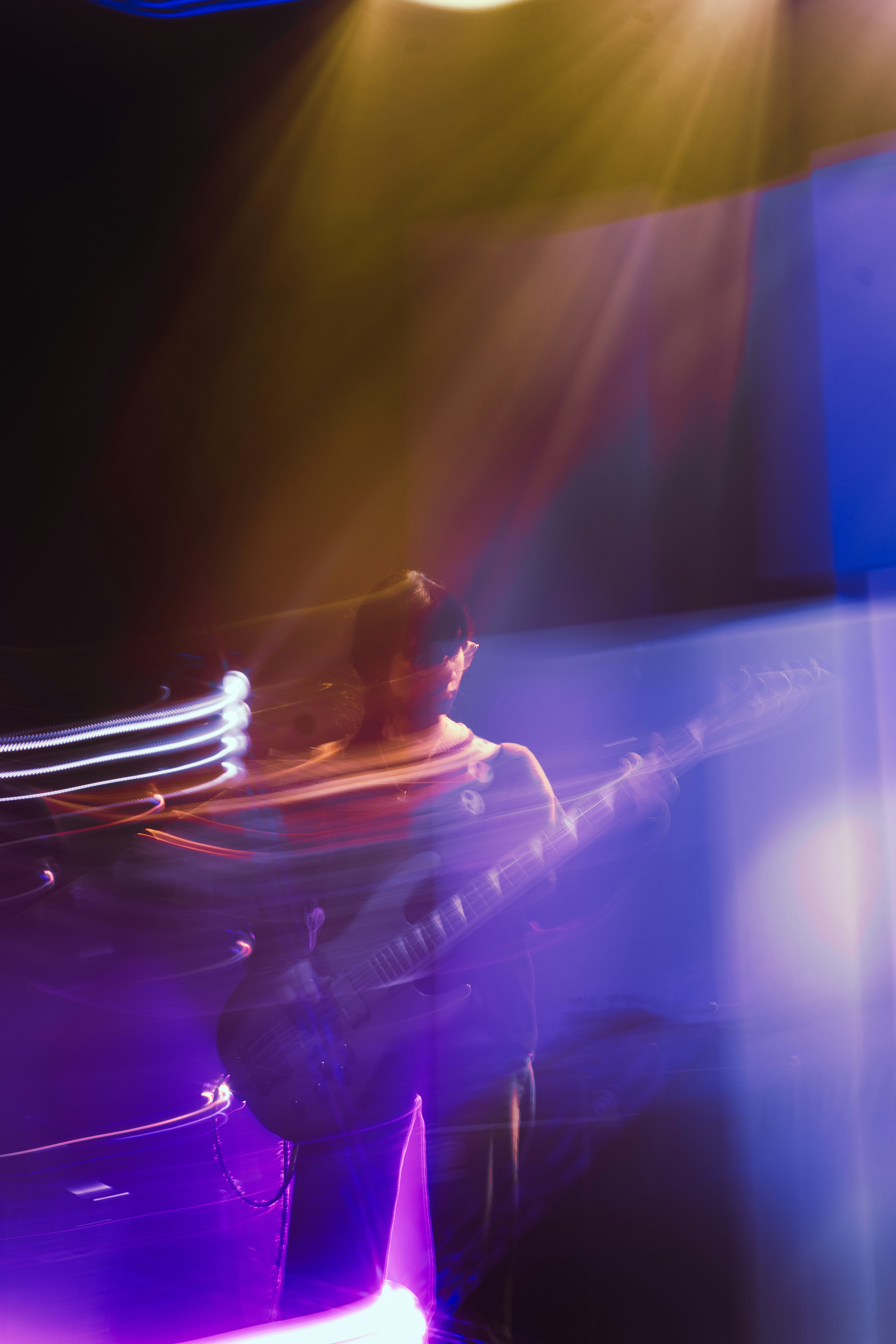 Musician passionately playing a bass guitar under vibrant stage lights, creating a dynamic blend of colors and motion.