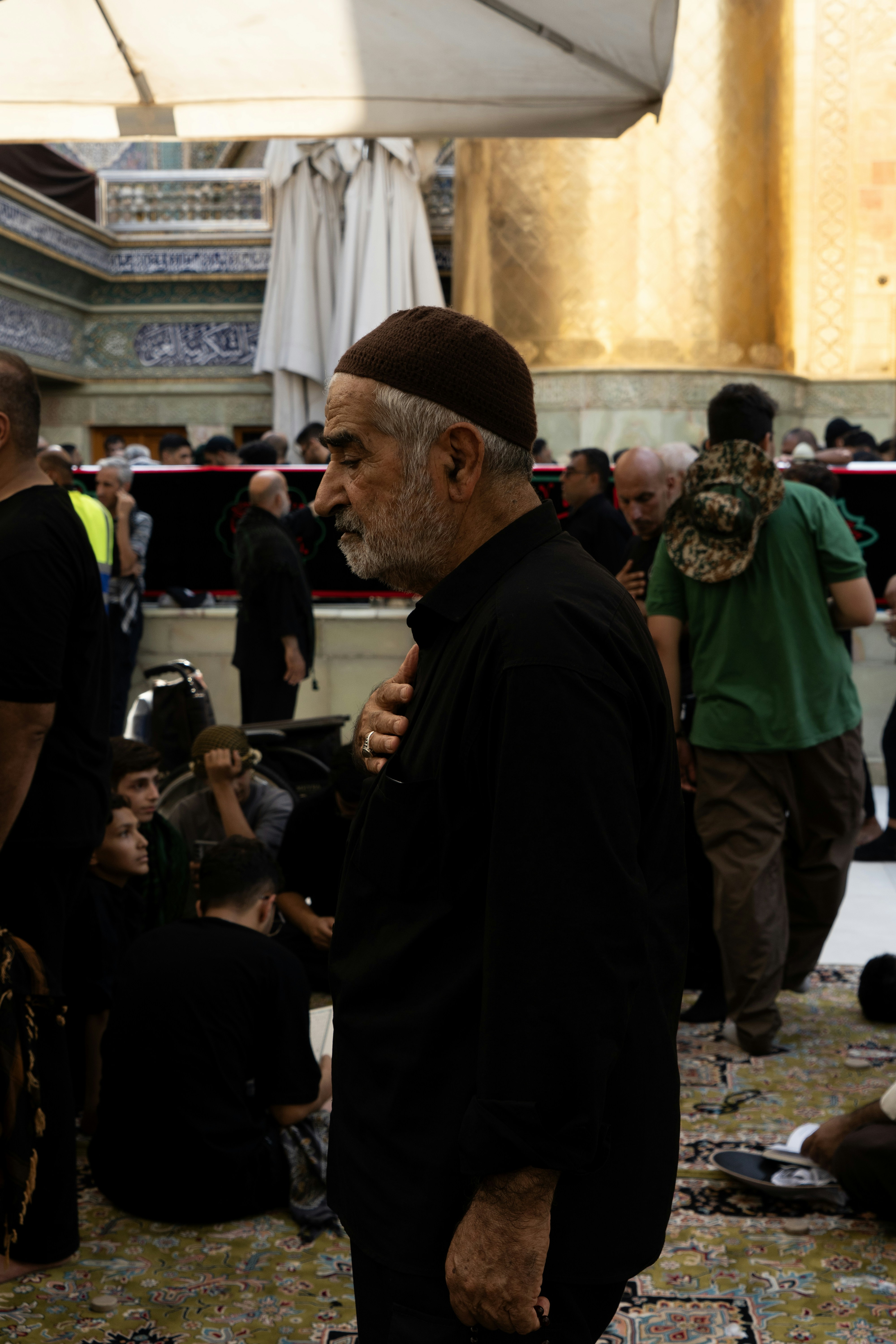 Elderly man in traditional attire stands thoughtfully among a crowd in a sacred space, symbolizing contemplation amidst communal devotion.