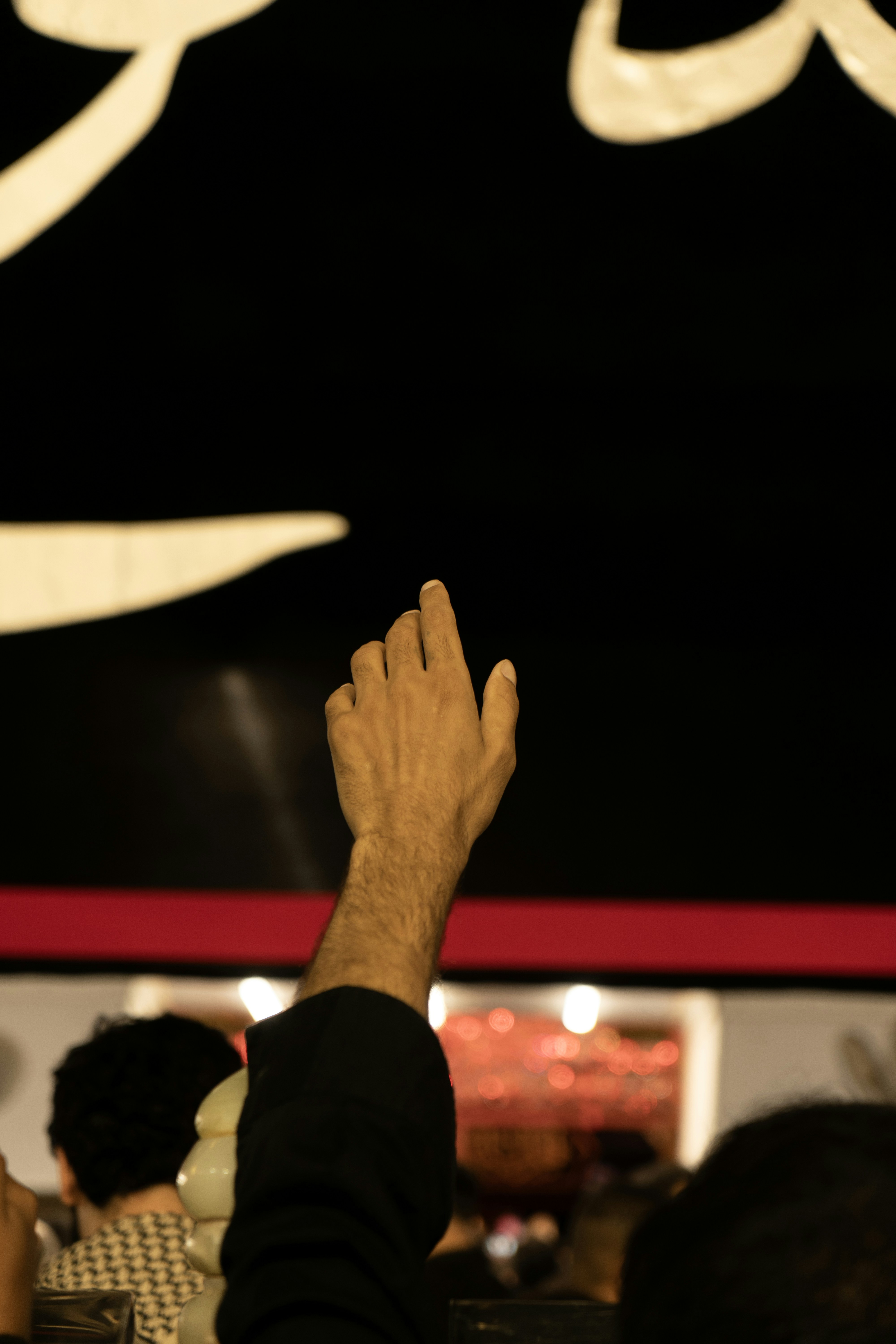 Gesture in the Gloom: A Raised Hand Before a Gold Logo Backdrop