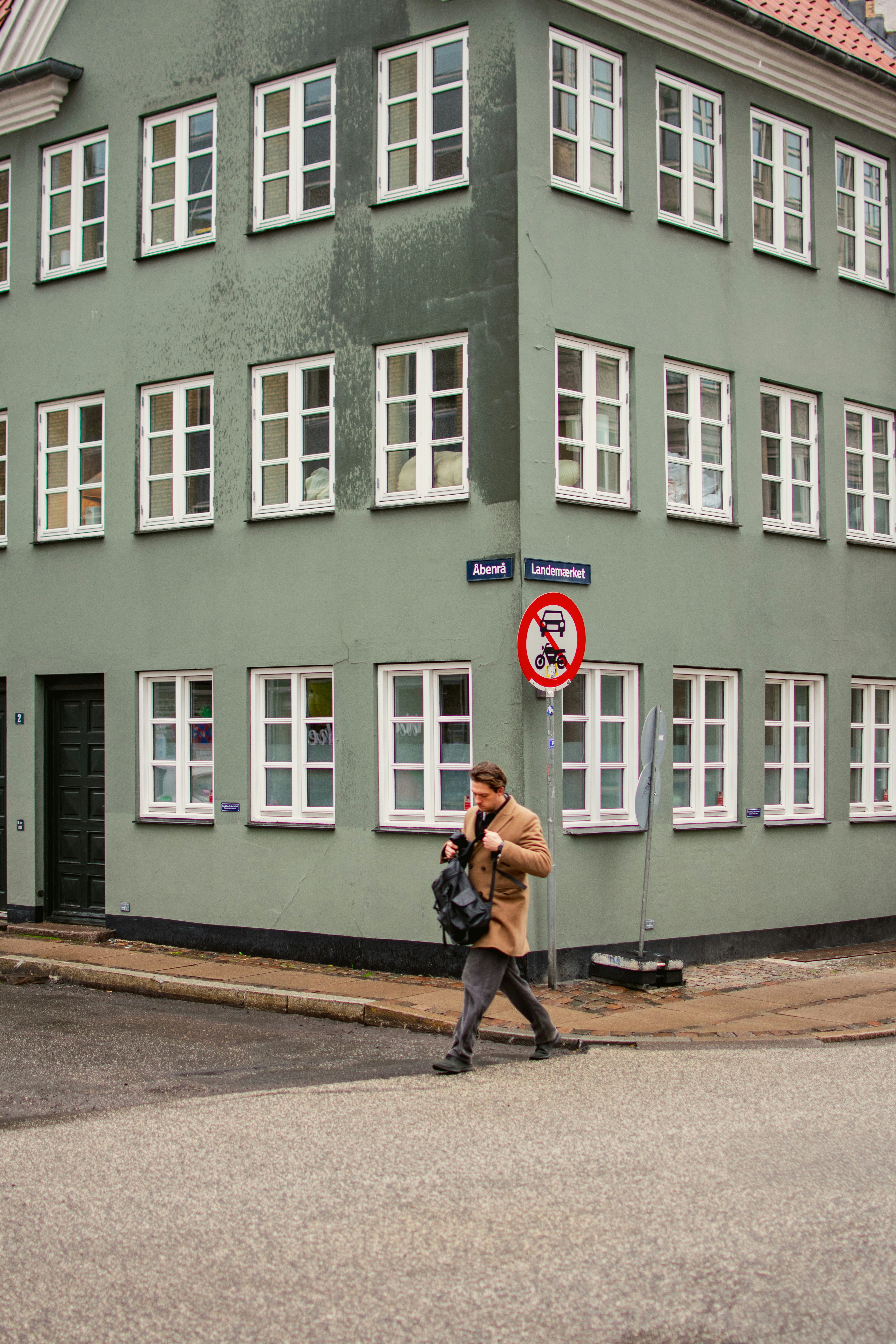 Man walks past a light green building on a street.