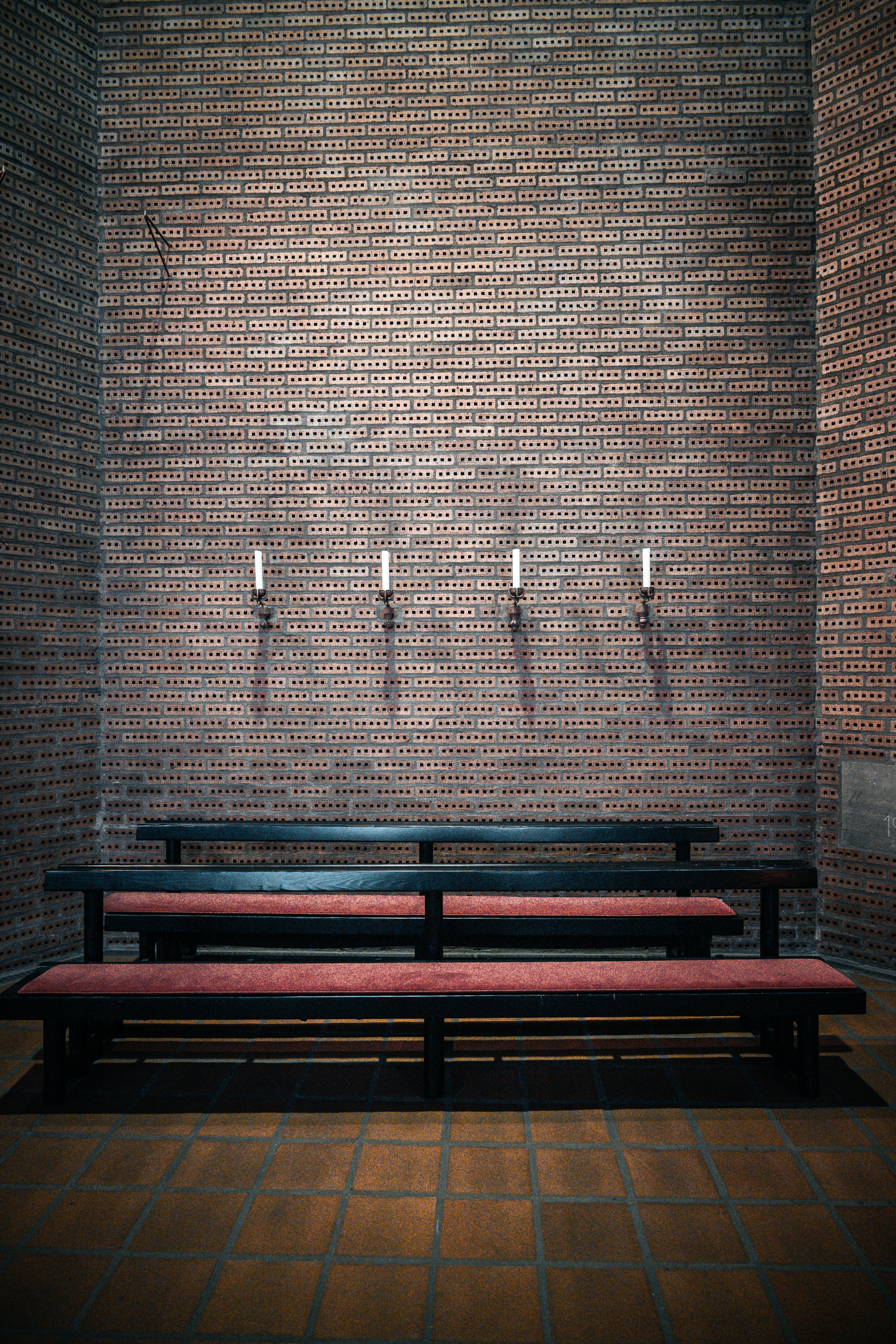 Brick-Walled Quiet: Five Hooks Above Red Benches in Dim Light