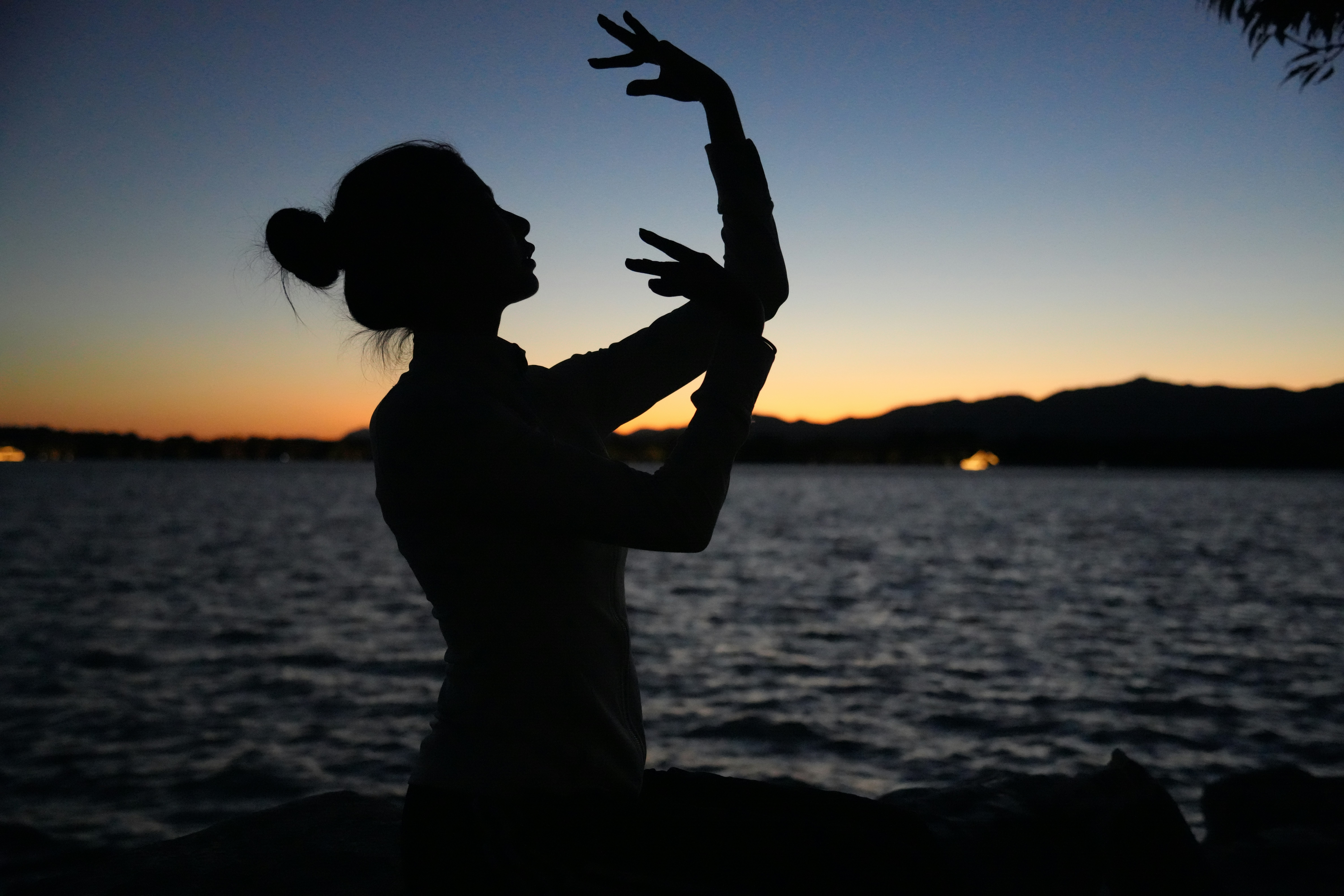 Silhouette of a dancer striking a pose against a twilight backdrop by the water's edge.