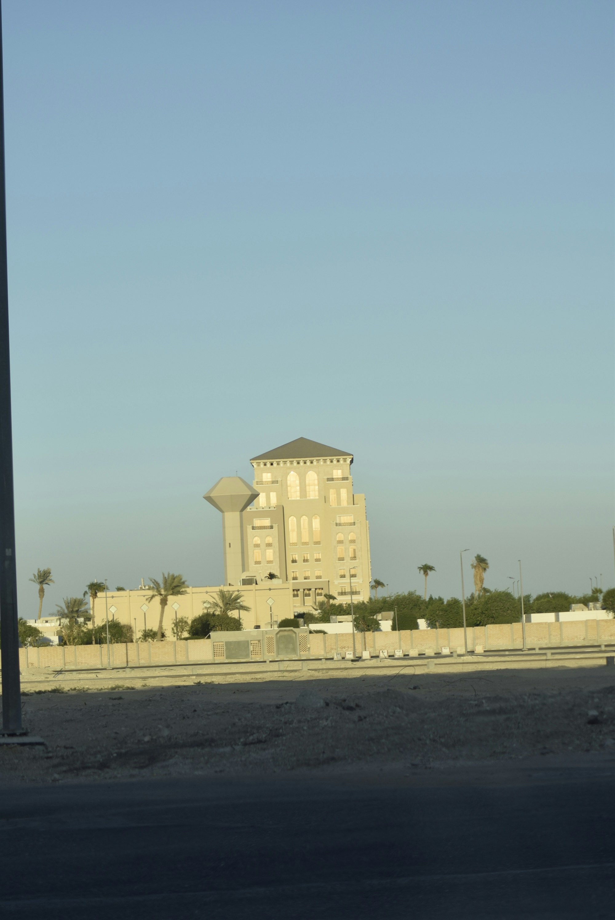 A striking modern building stands against a clear sky, surrounded by palm trees in a desert landscape.