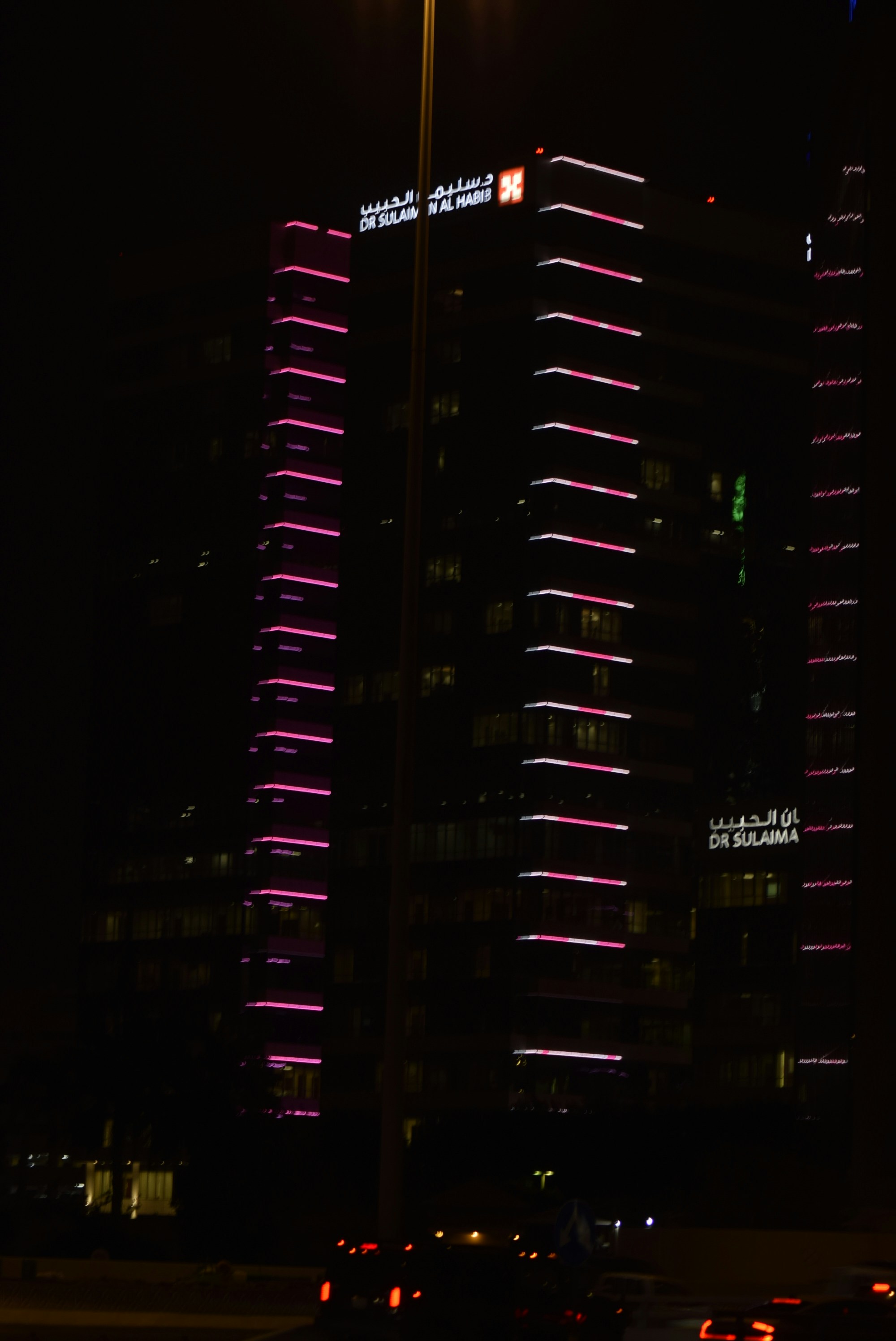Tall building illuminated with pink and white lights at night.