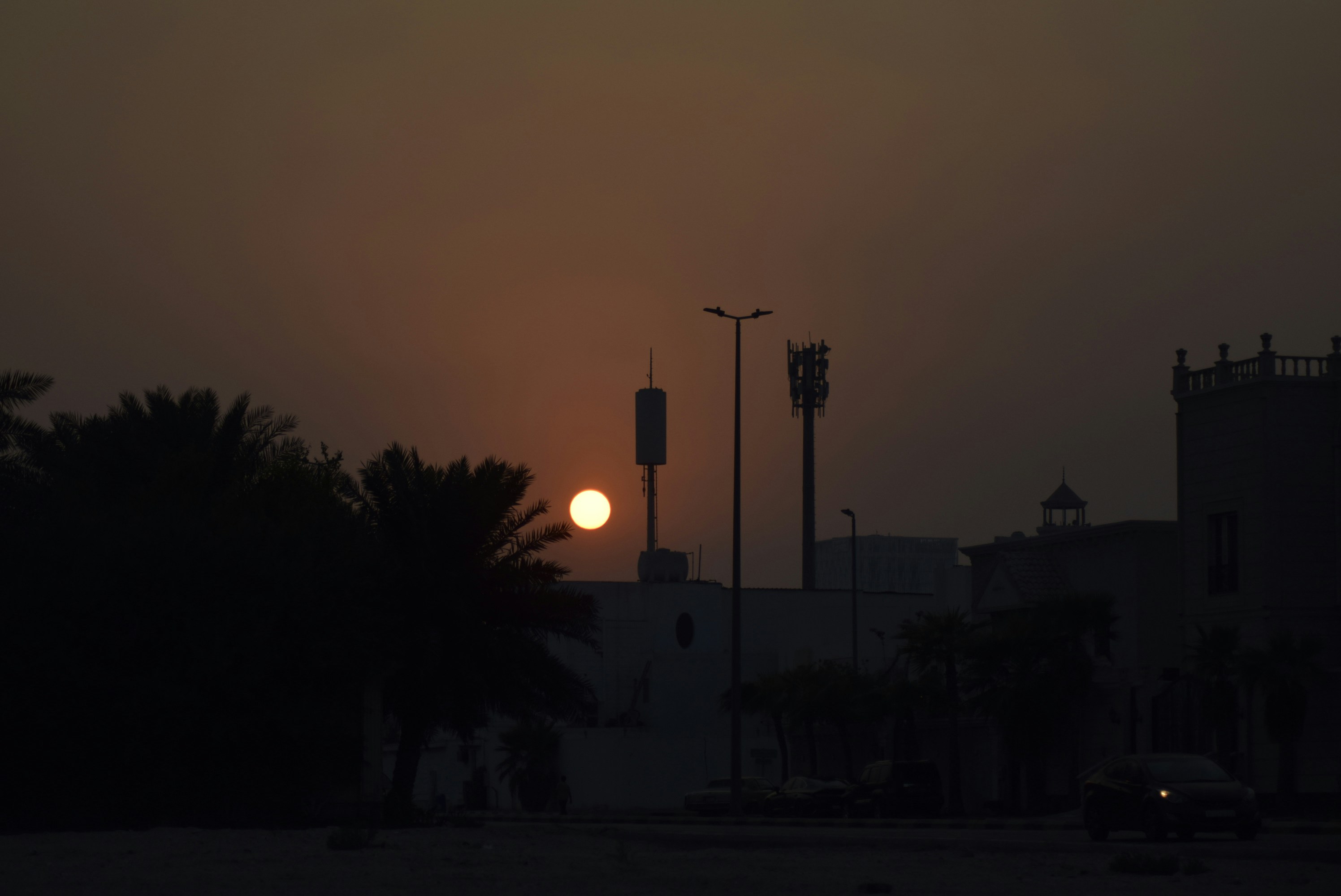 Silhouetted palm trees and buildings against a vibrant sunset sky, capturing the essence of a quiet evening in a desert landscape.