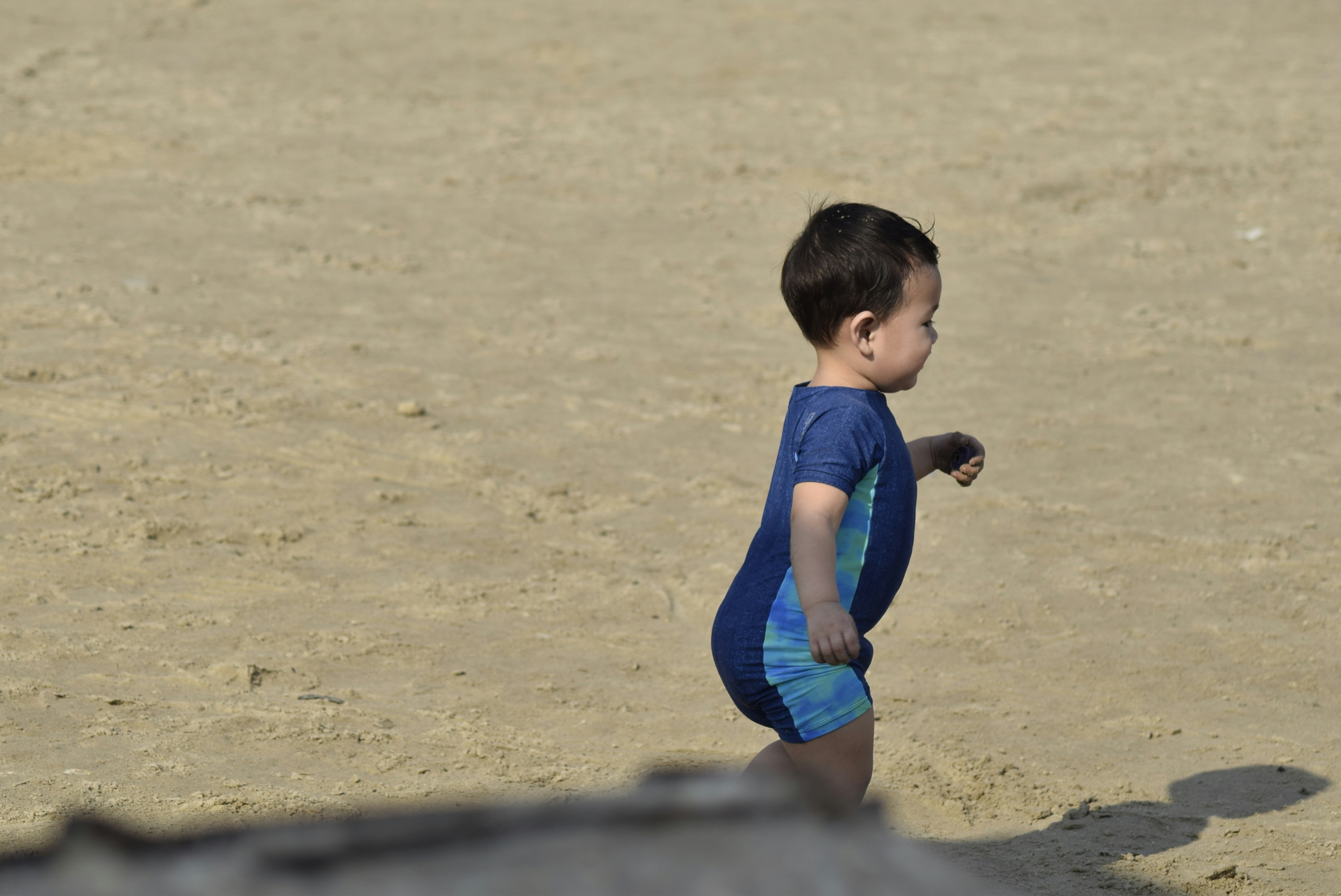 Seaside stride: a blue-suited toddler's sunlit walk