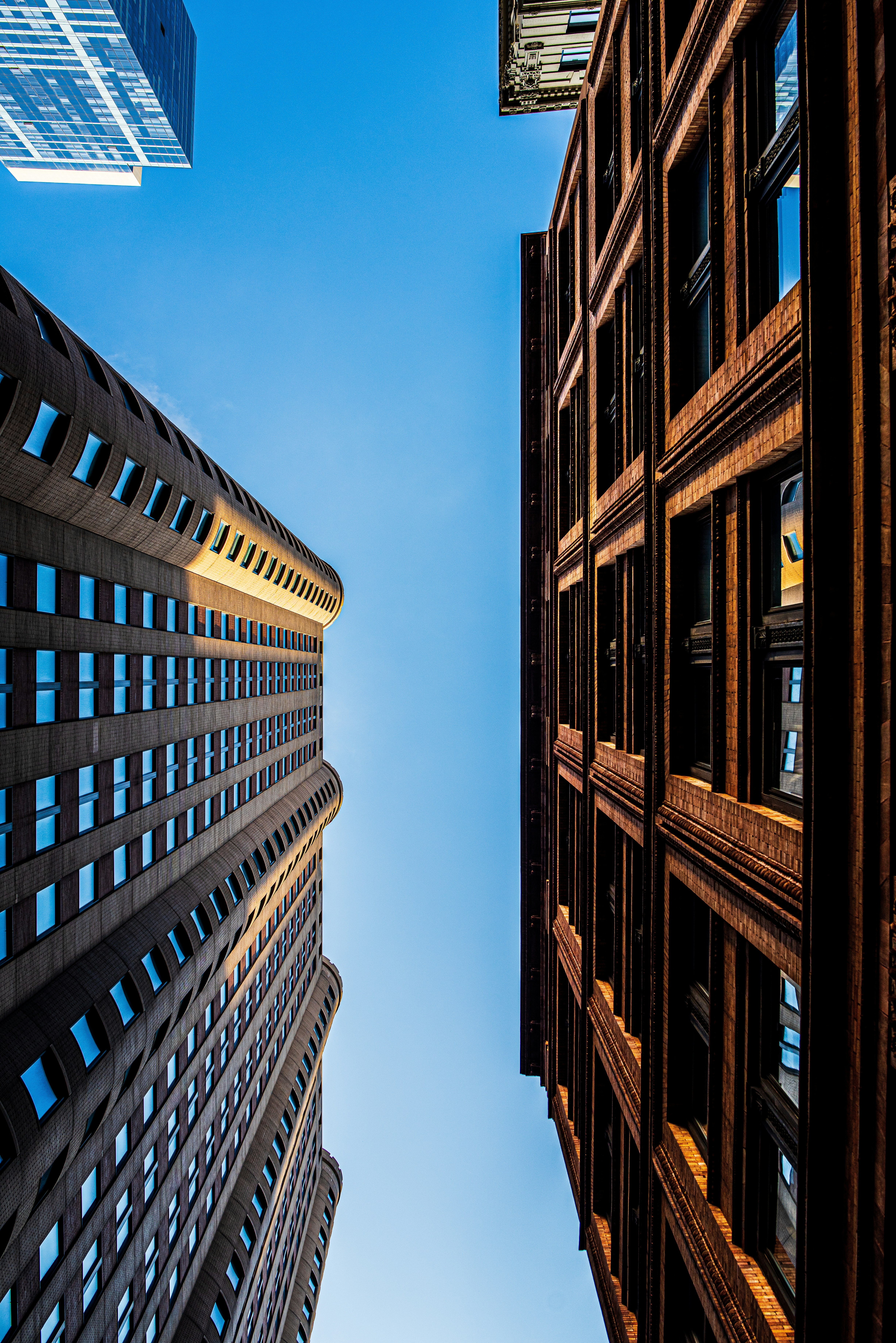 Looking up at tall buildings in the Financial District of lower Manhattan. | Two tall buildings against a clear blue sky.