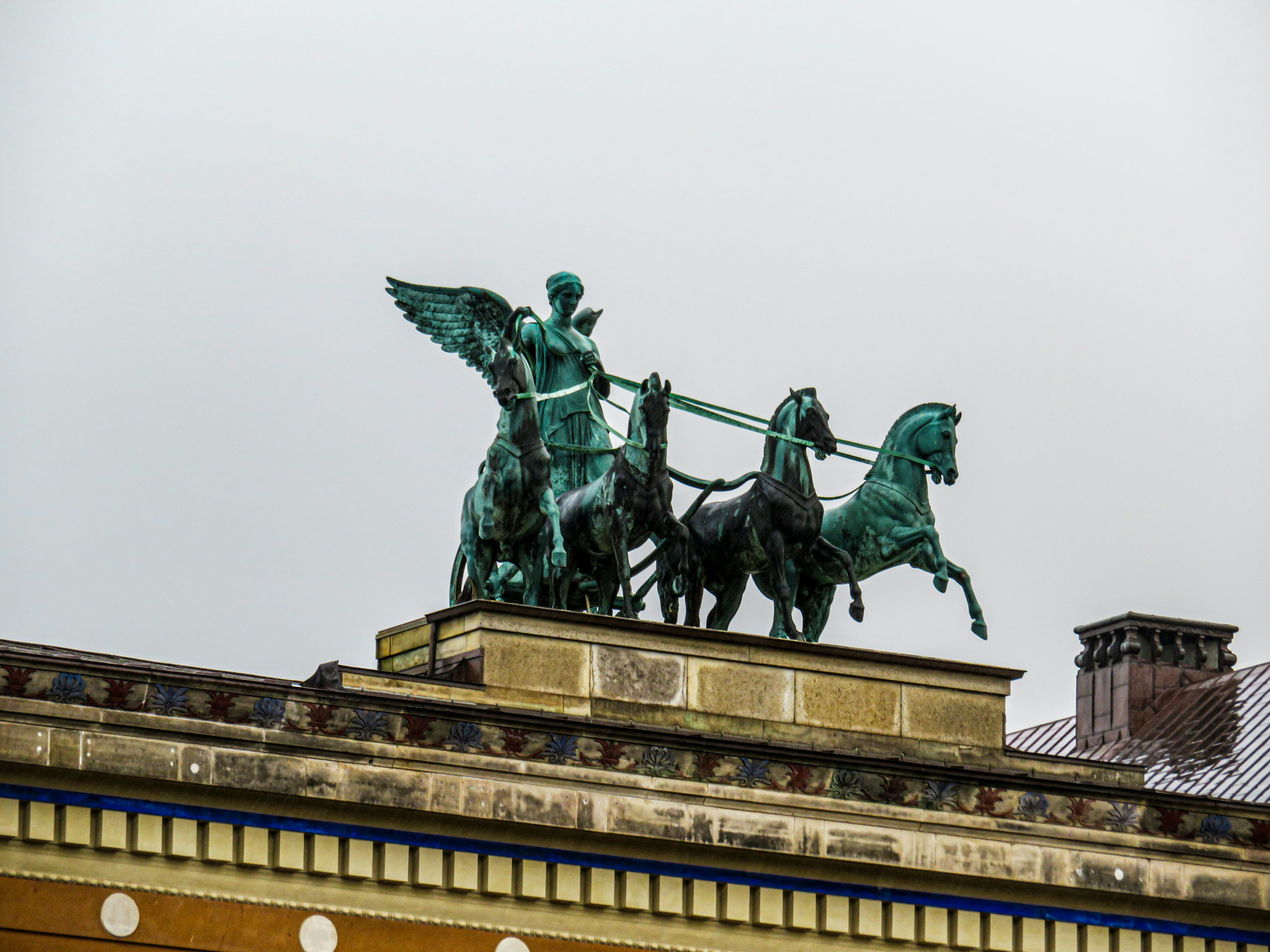 Bronze sculpture of a charioteer guiding four horses atop a historic building, showcasing classical artistry against a cloudy sky.