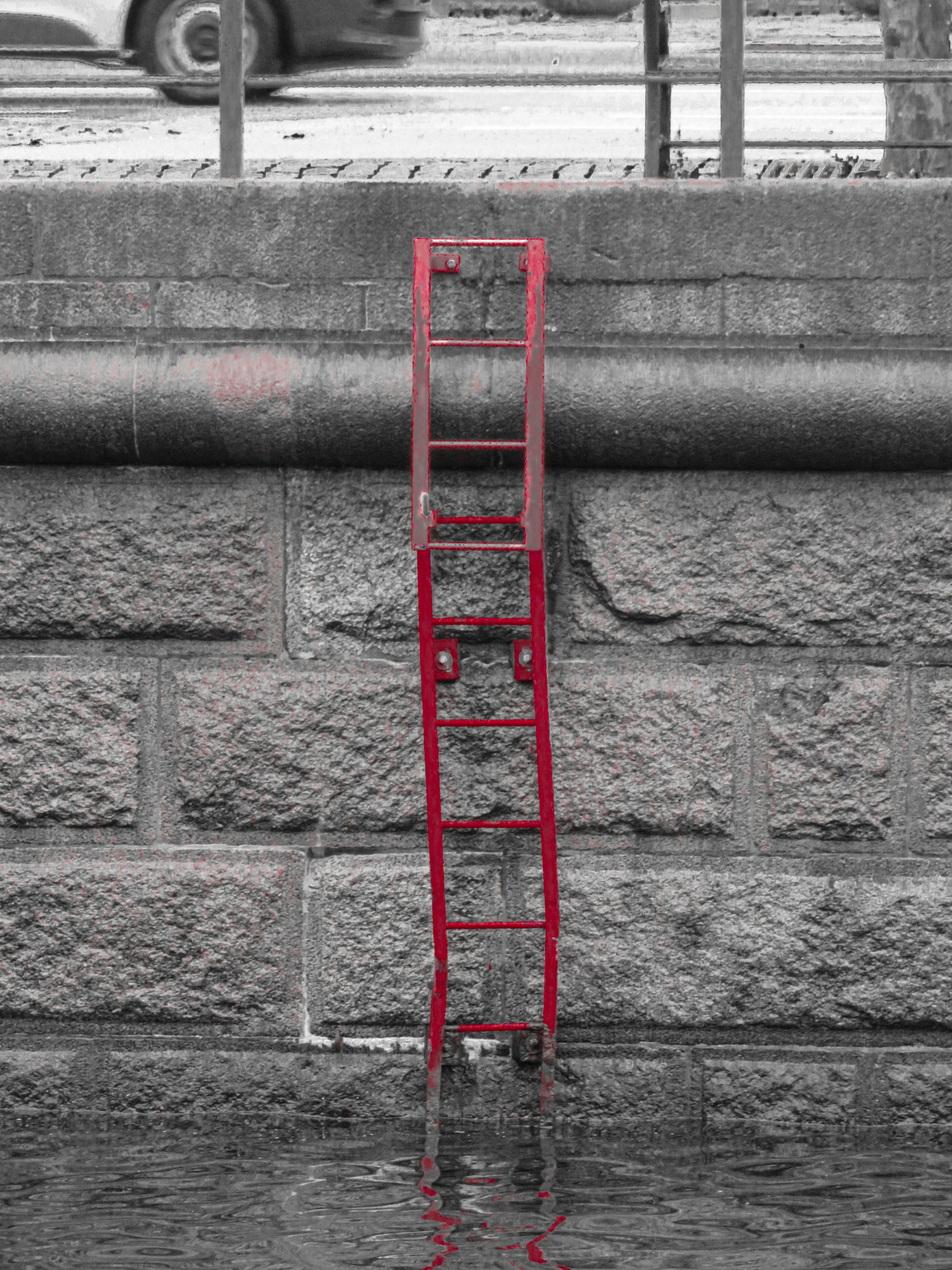 Red ladder partially submerged in water against stone wall