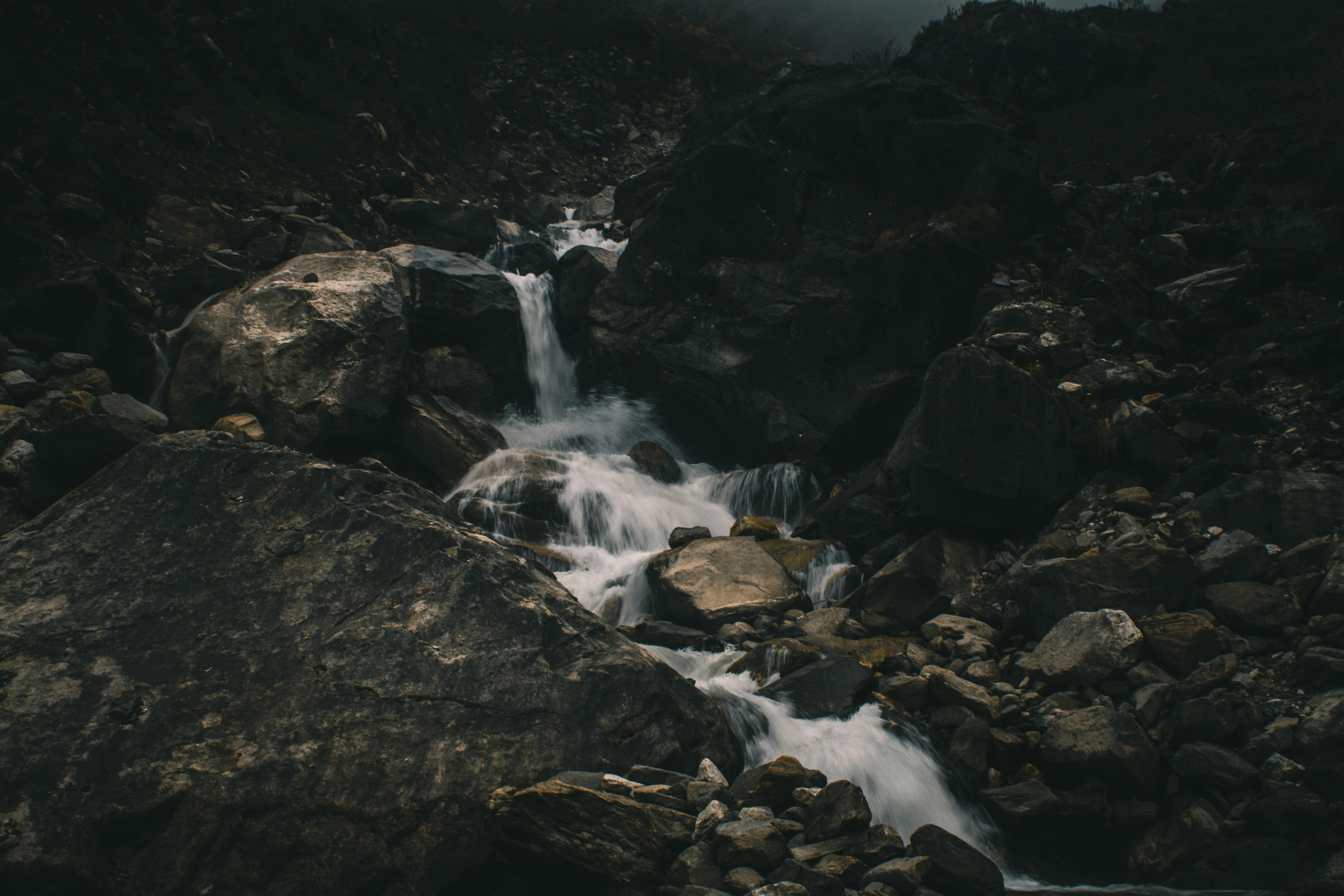 A rocky mountain stream flows downhill through dark boulders. photo ...