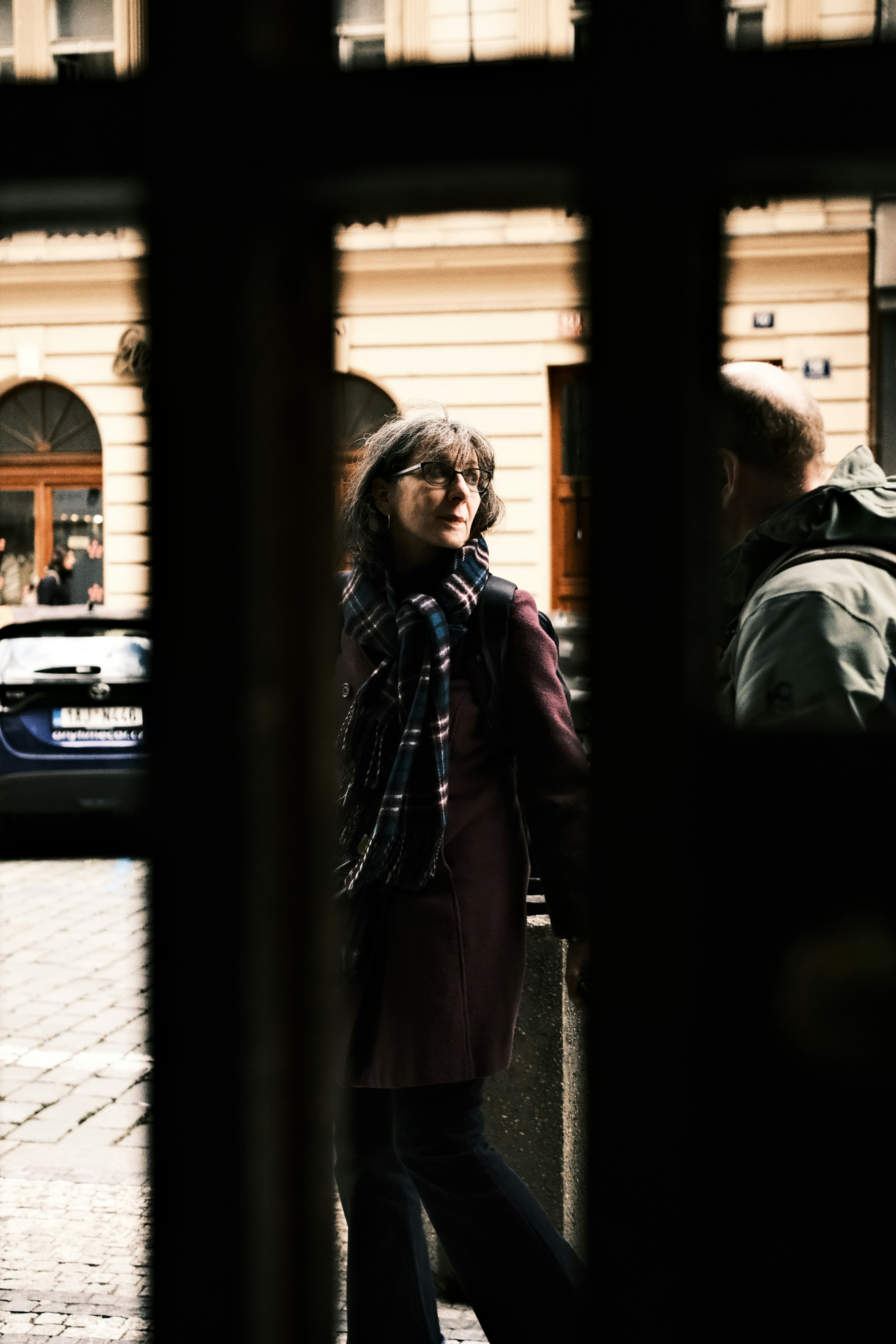 Woman is turning back when walking on a street. | Woman wearing a scarf walks down a street.