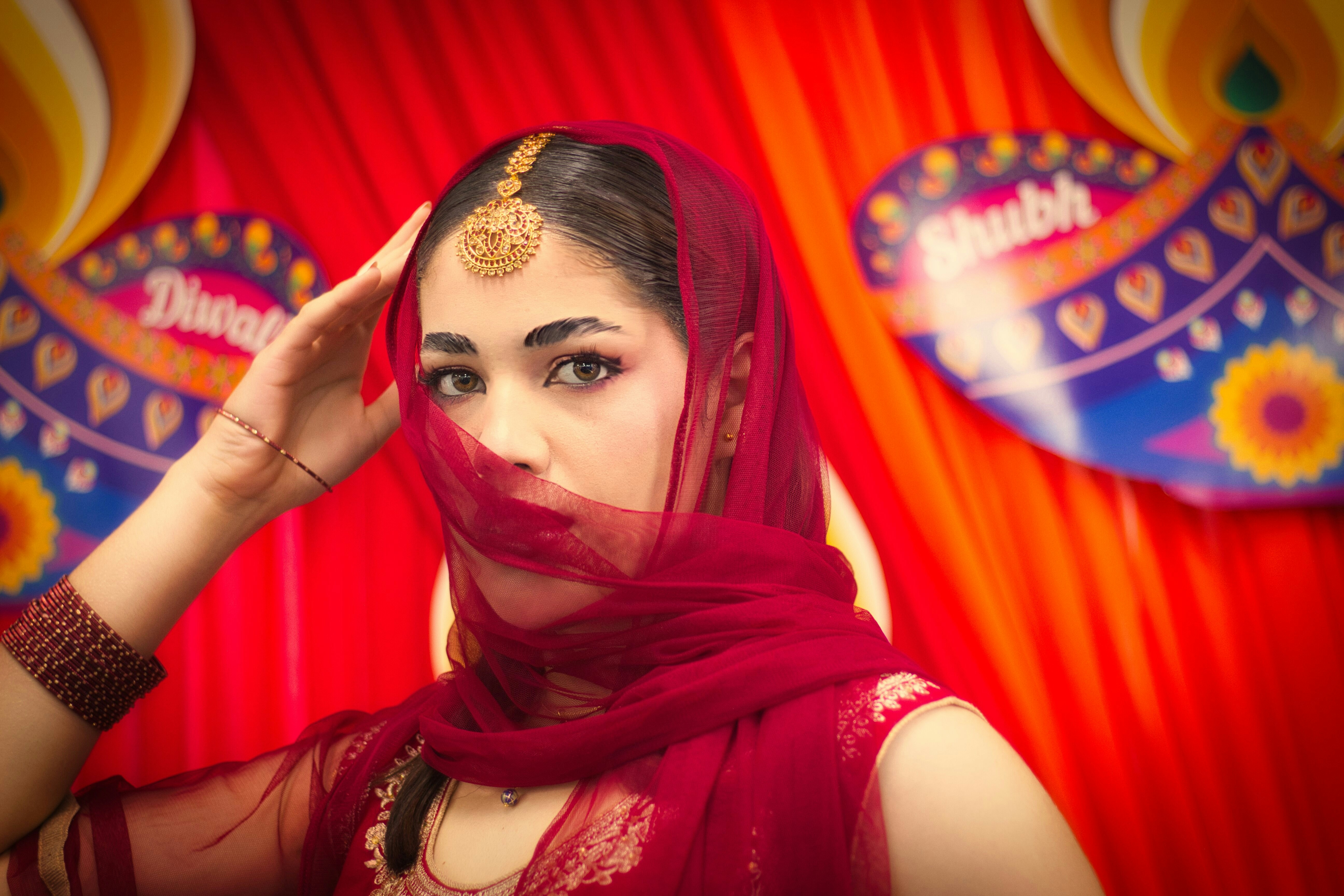 Young woman adorned in traditional attire, partially veiled, against a vibrant backdrop celebrating cultural festivities.