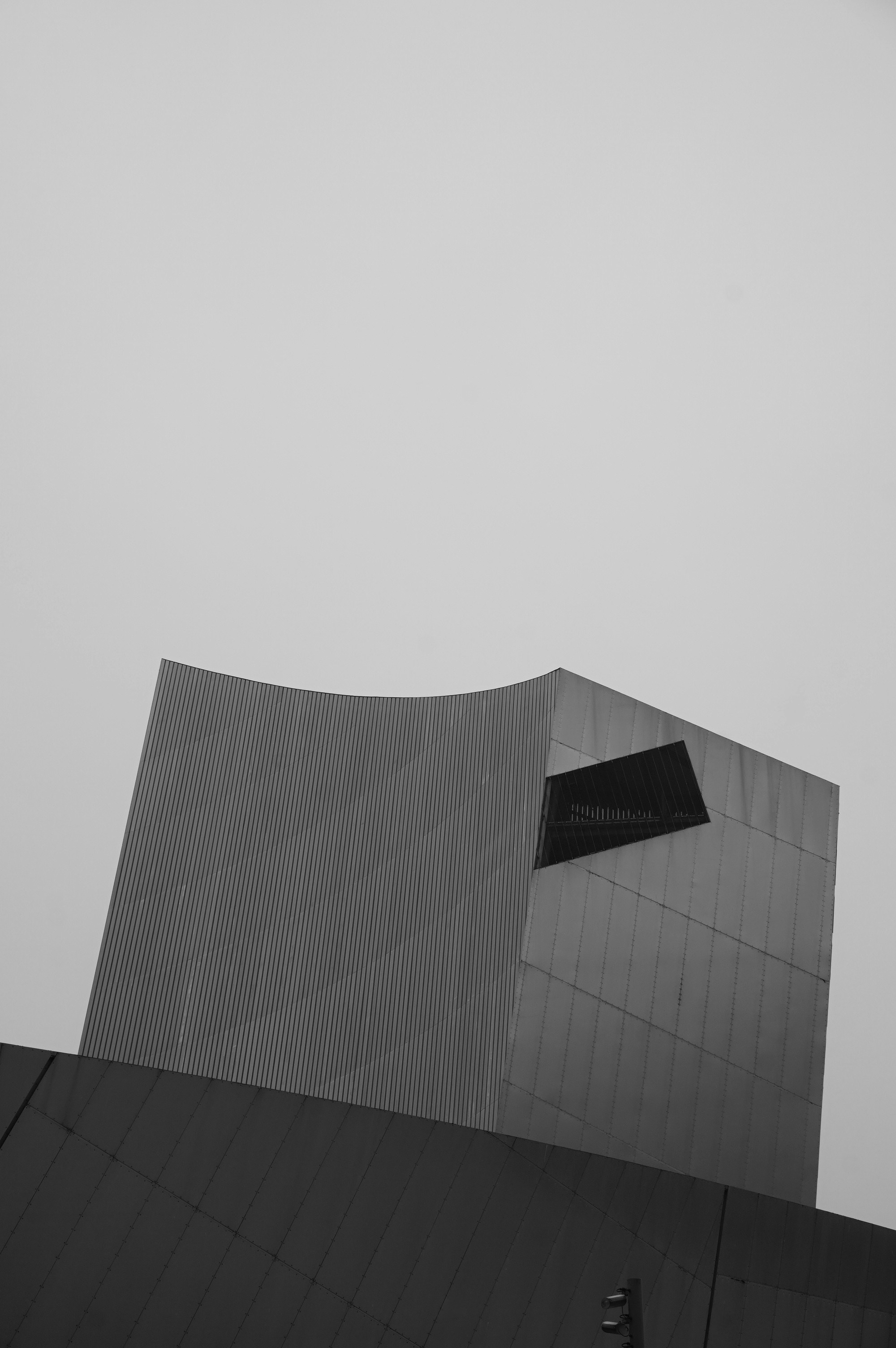 Abstract view of a modern building with sleek lines and geometric shapes, highlighted against a gray sky.