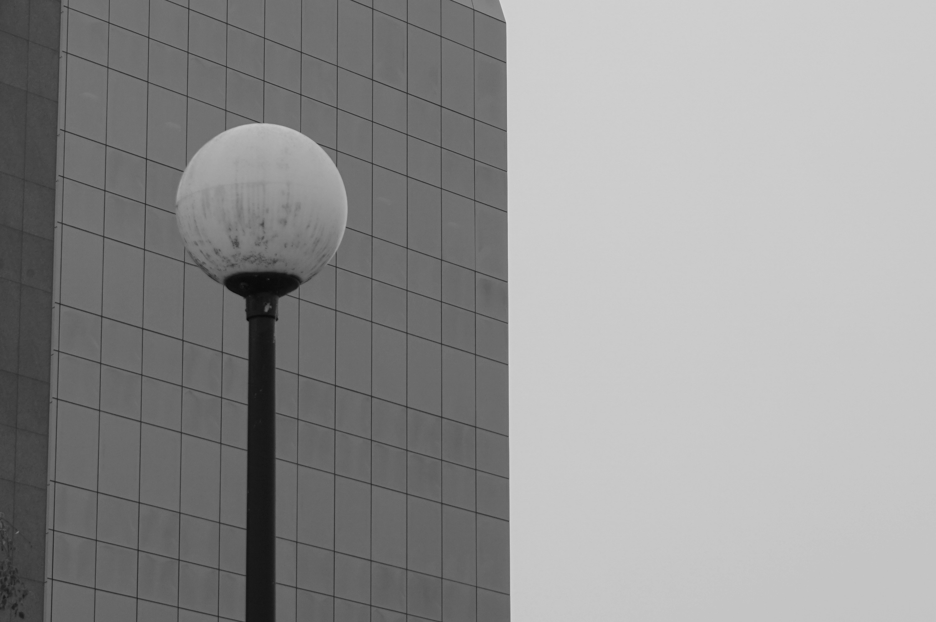 A lone streetlight stands against a backdrop of a modern glass building, showcasing a stark contrast in textures and tones.