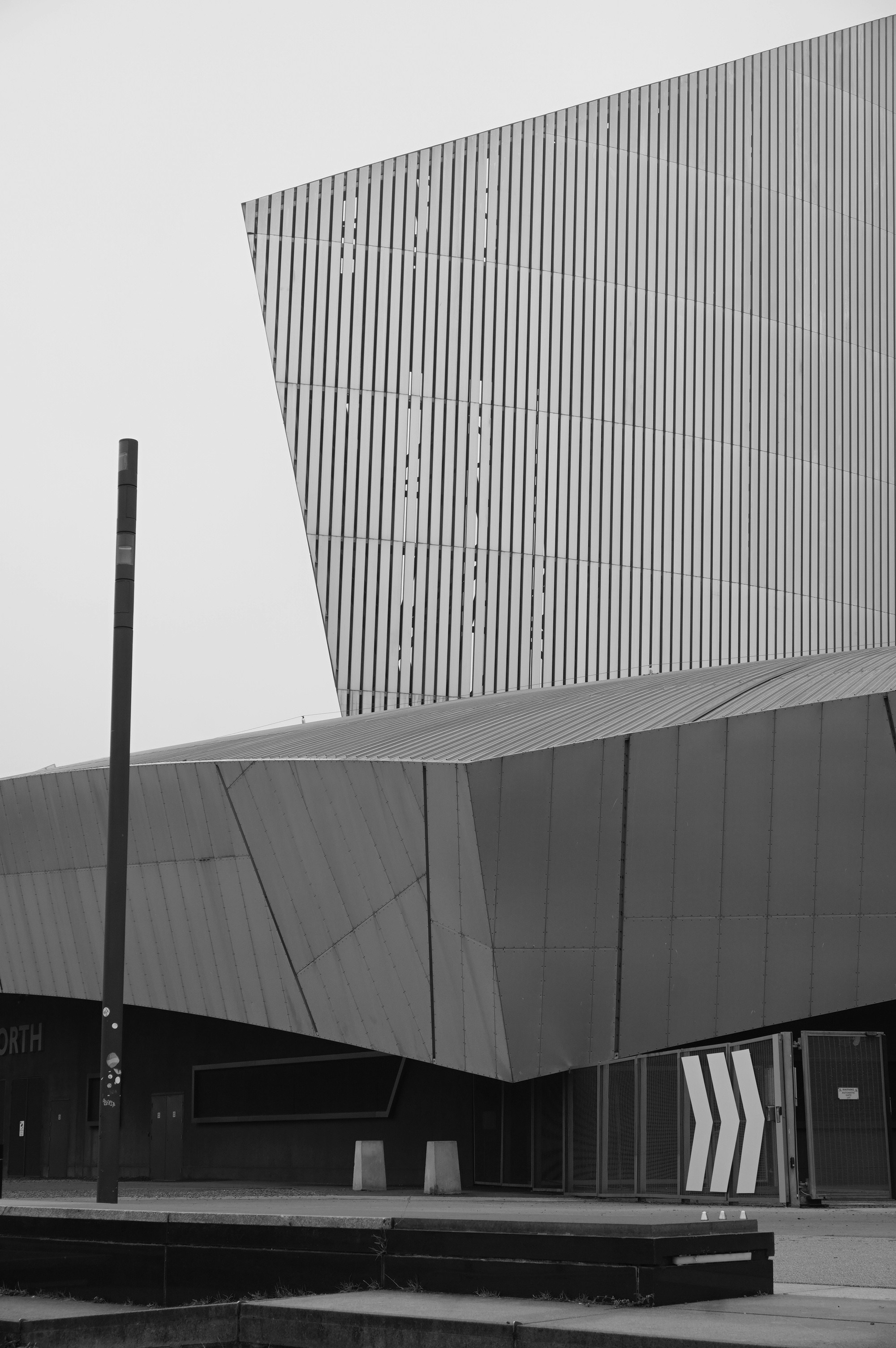 Abstract architectural structure featuring sharp angles and metallic surfaces under a cloudy sky.