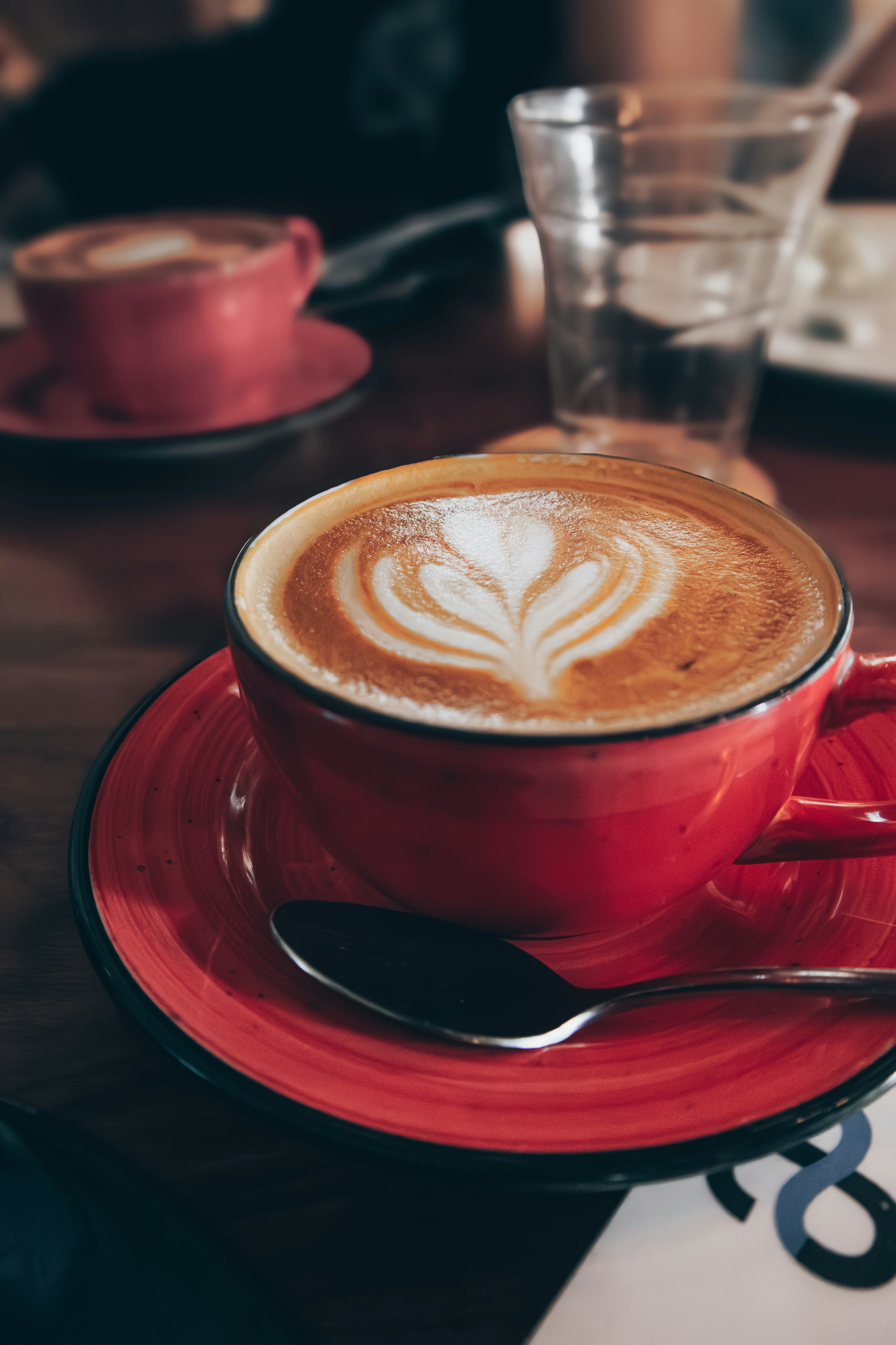 Red cup with latte art and spoon on saucer