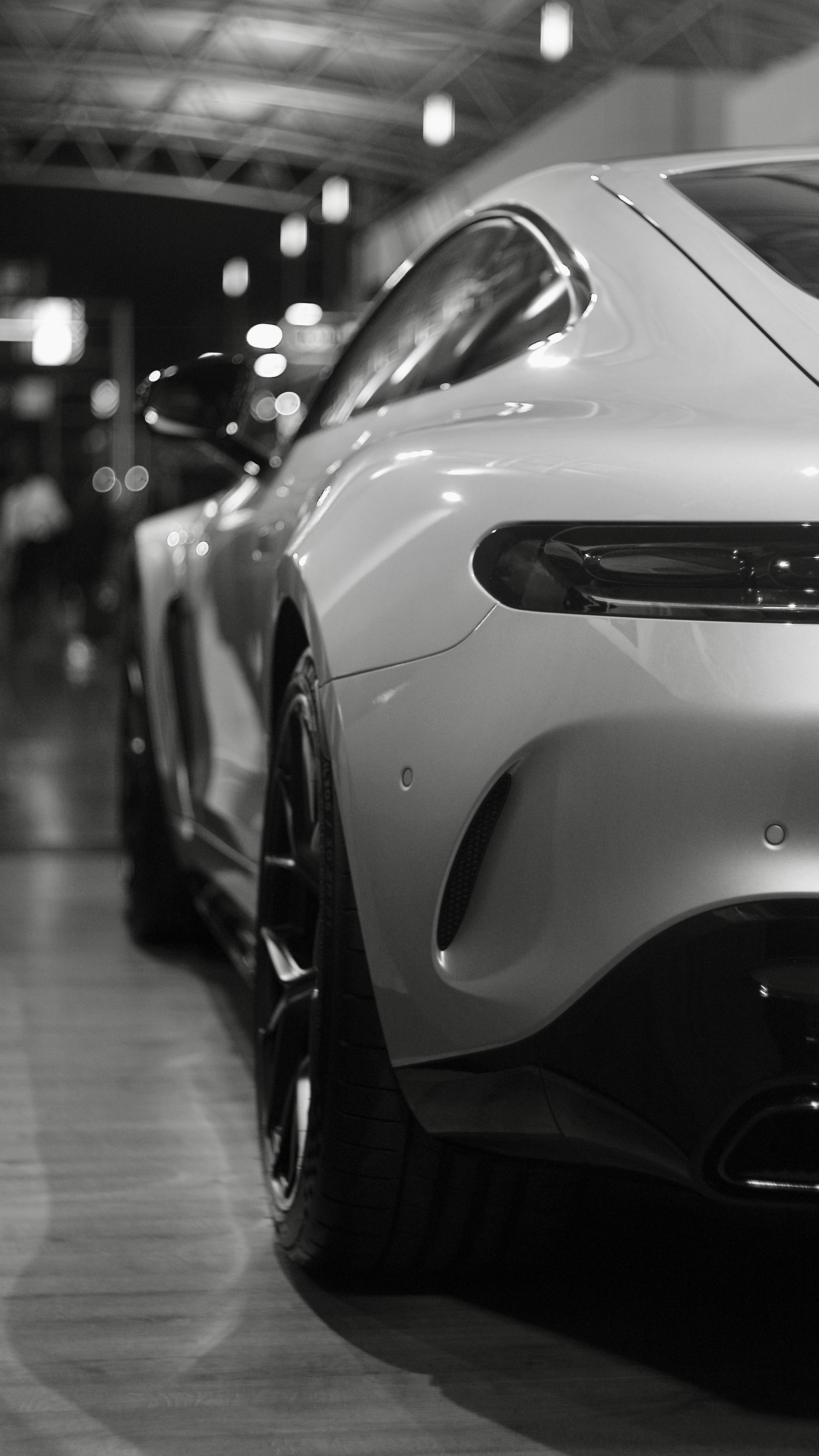 Sleek silver sports car captured from a low angle, highlighting its aerodynamic curves and stylish design. The background features a blurred exhibition setting.