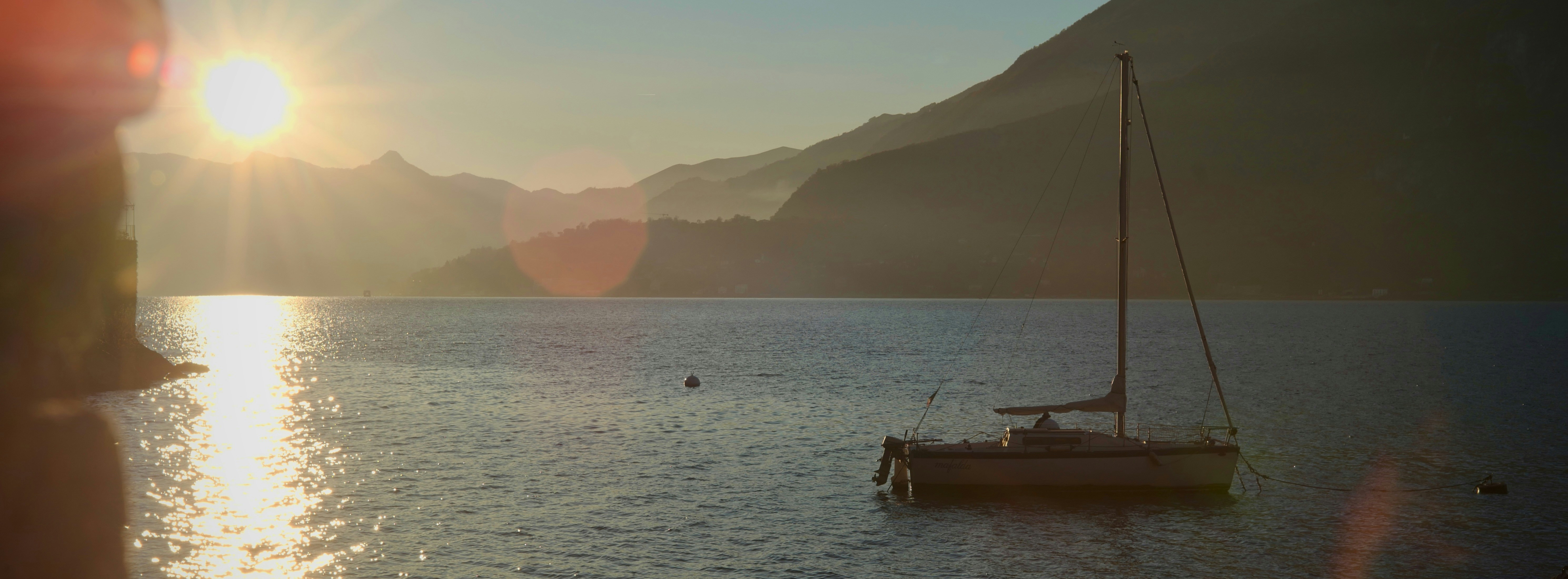 Sailboat on a calm lake at sunset with mountains.