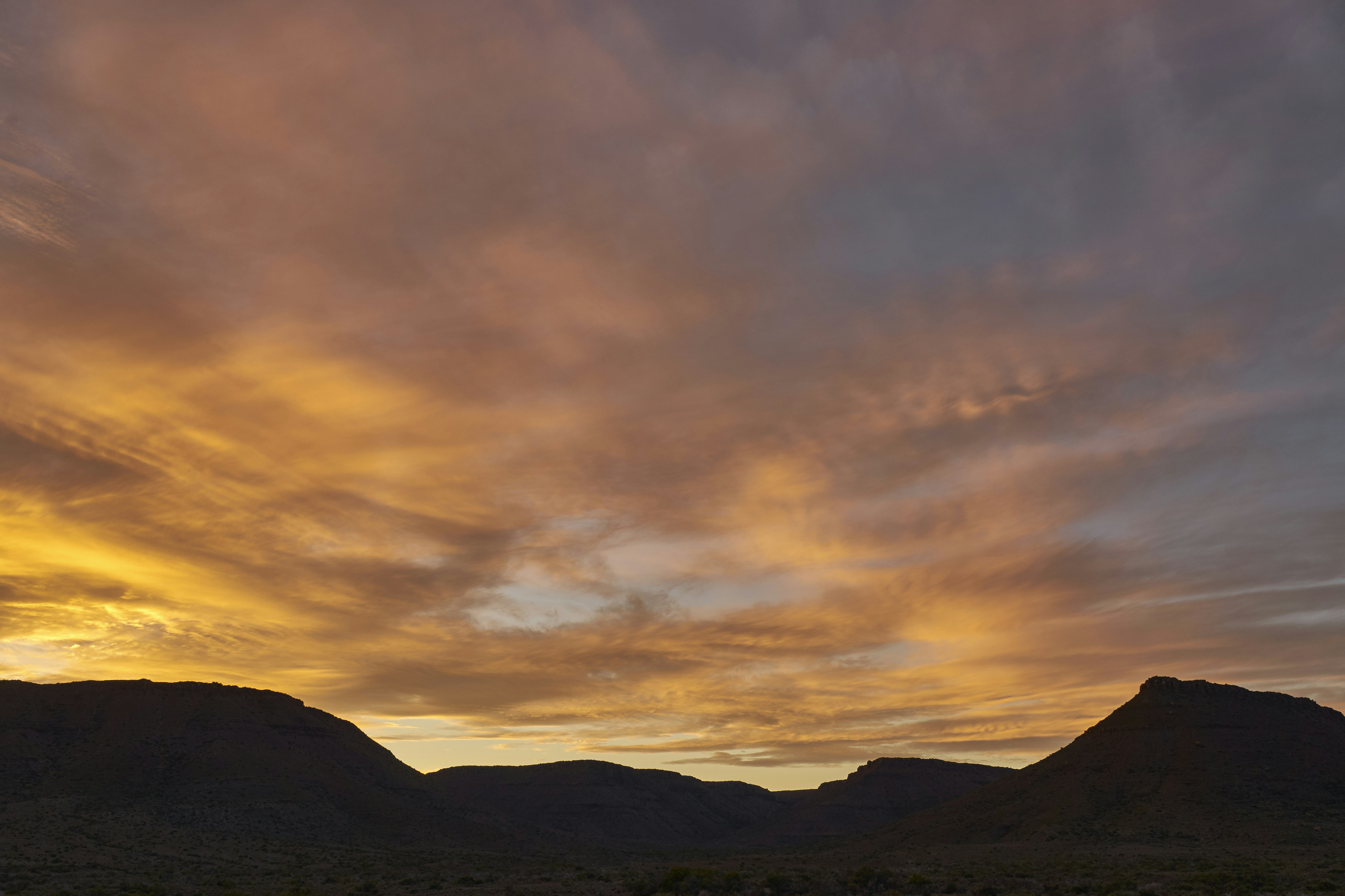 Vibrant sunset colors blend across the sky, silhouetting rugged mountain outlines in a tranquil desert landscape.