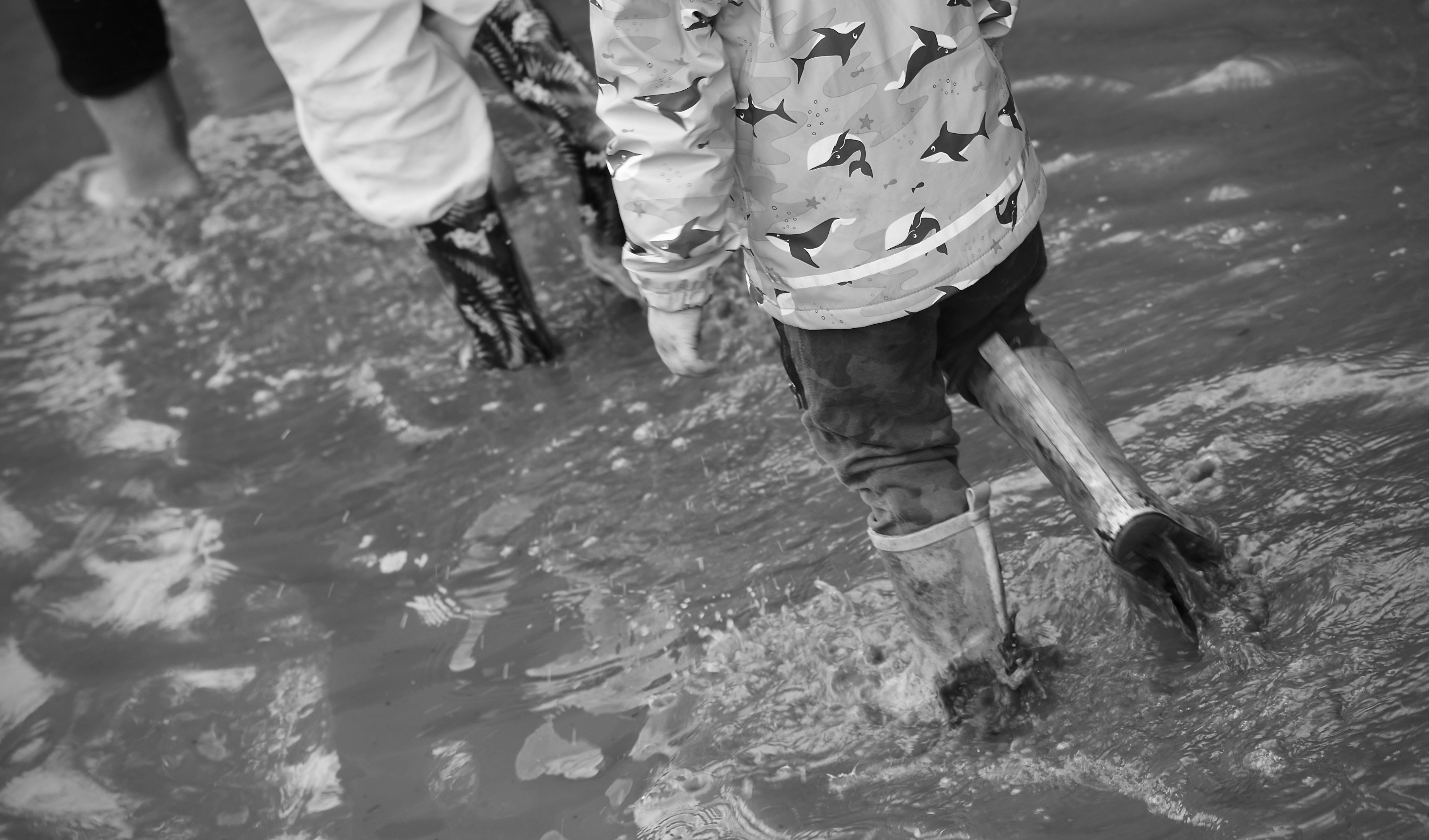 Children wearing rain boots wading through muddy water
