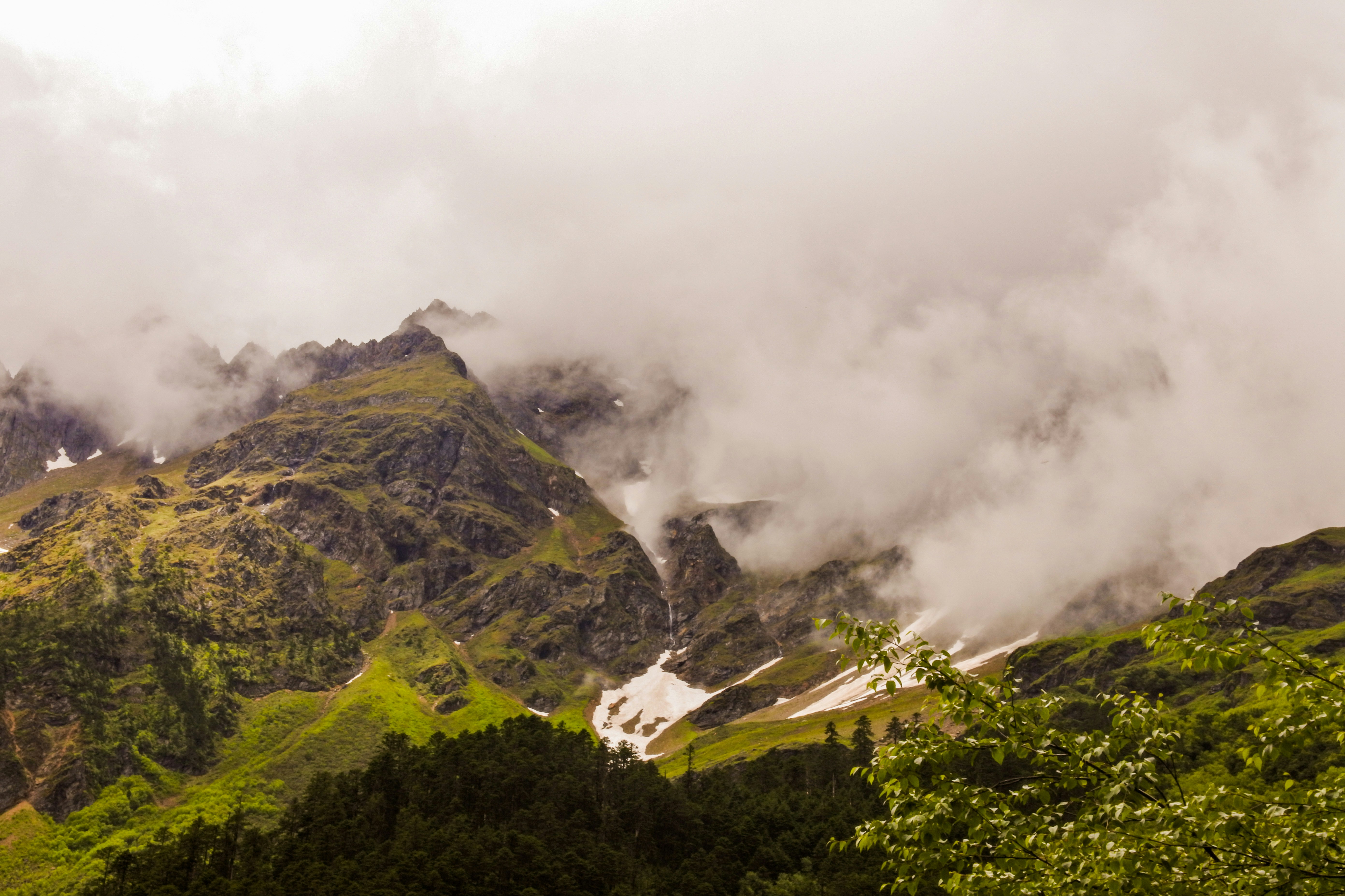 Misty clouds obscure rugged mountain peaks with green slopes.