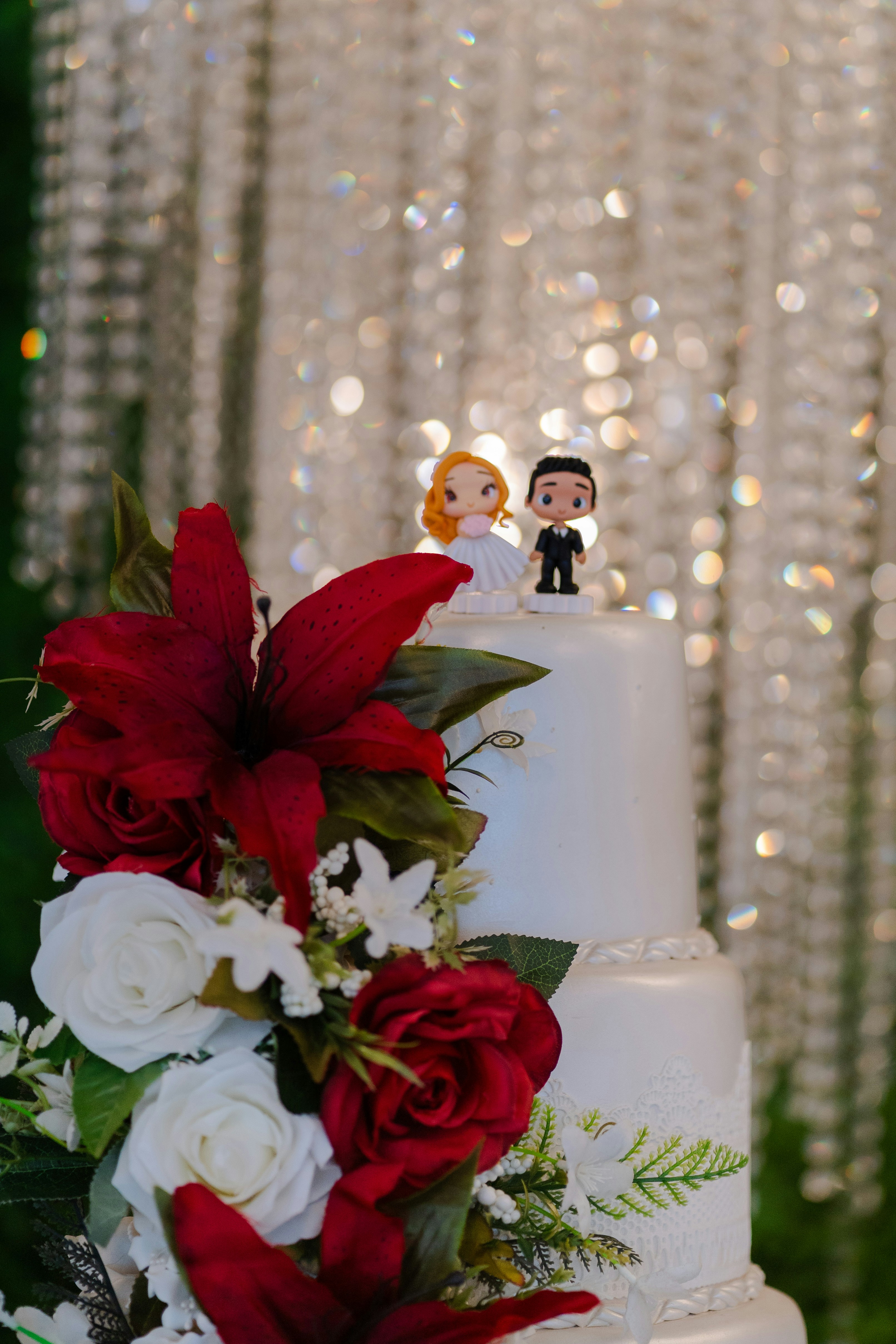 Topper Portraits Among Crimson Roses on a Wedding Cake