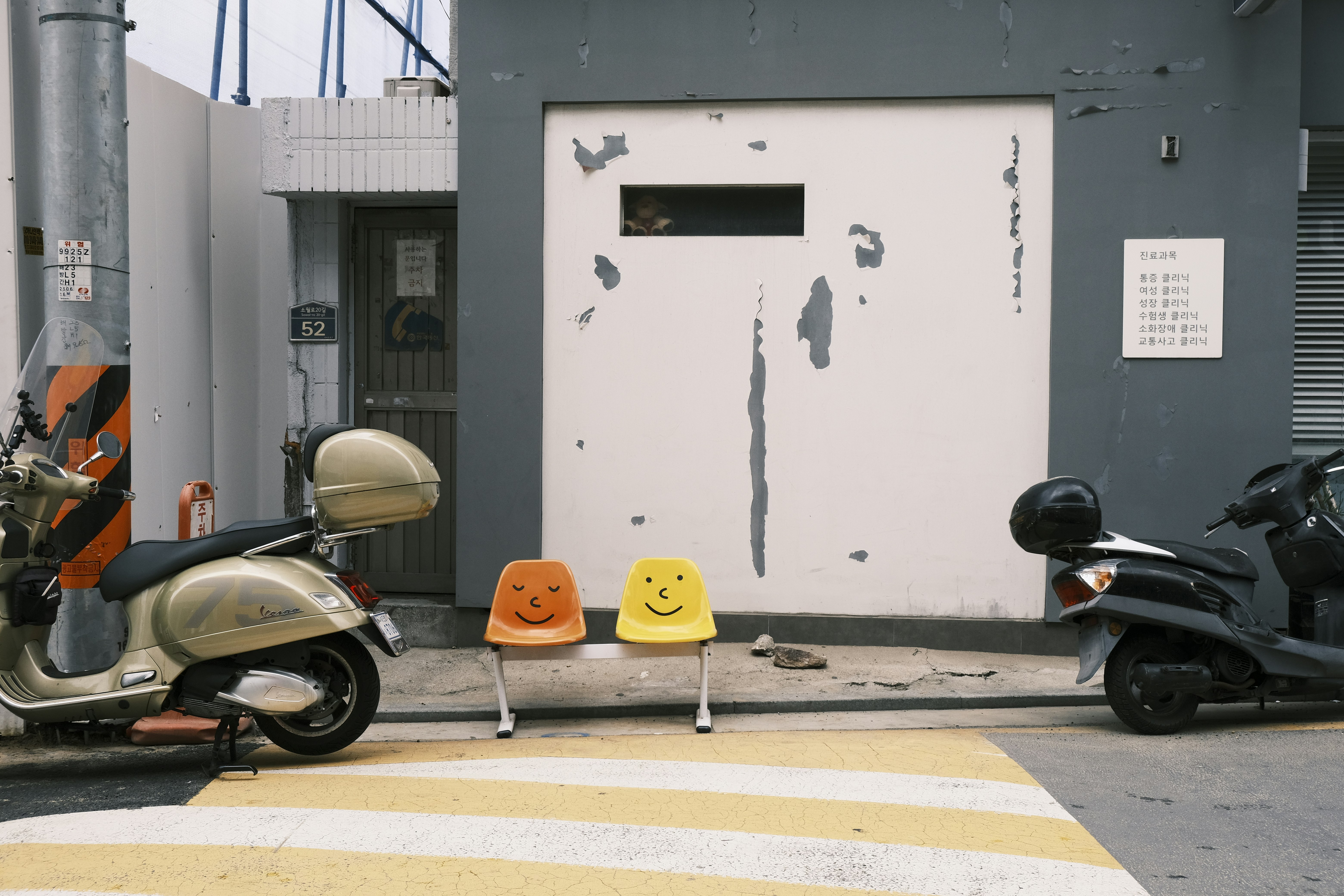 Two Smiling Stools Stand Between Scooters Before a Weathered Urban Wall